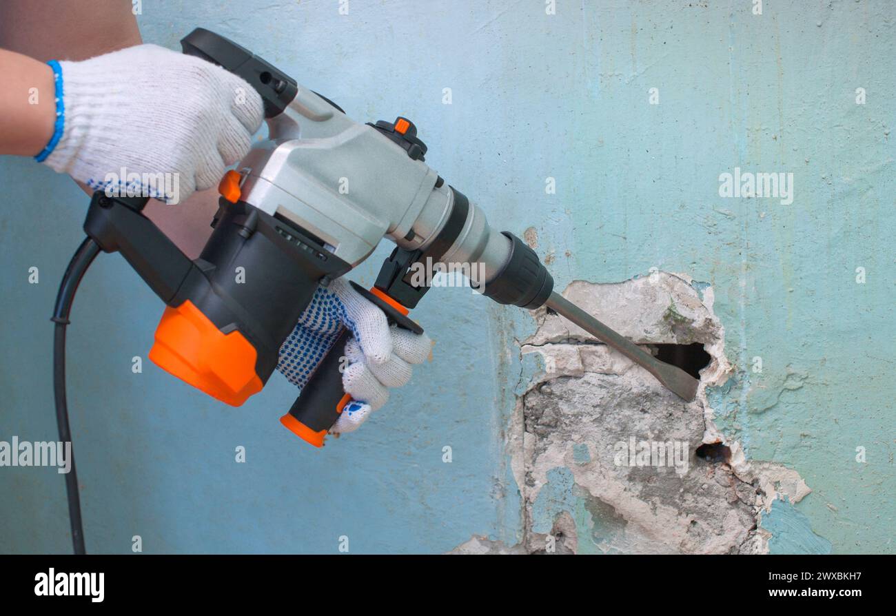 The builder with hammer drill perforator equipment making hole in wall ...