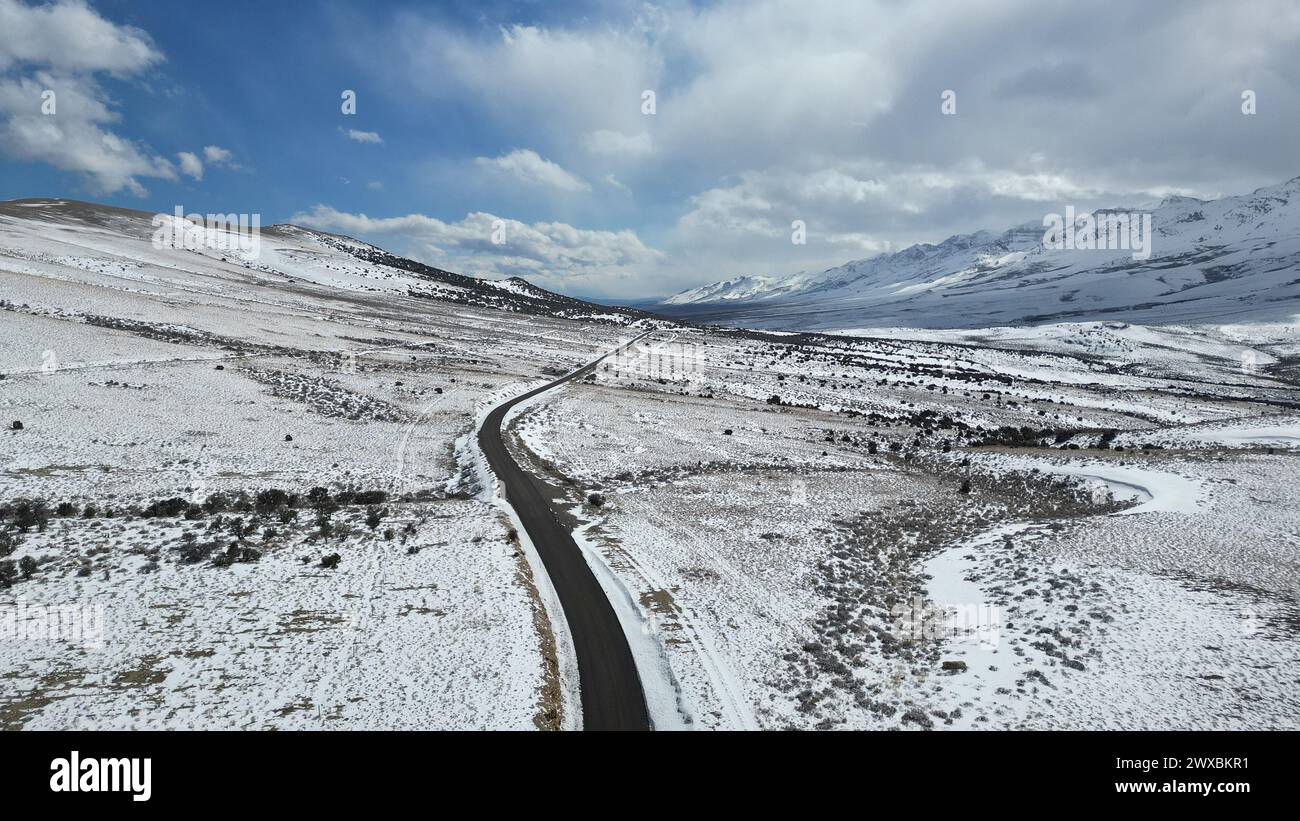 A long narrow snowy road descending a hill with distant mountains in ...