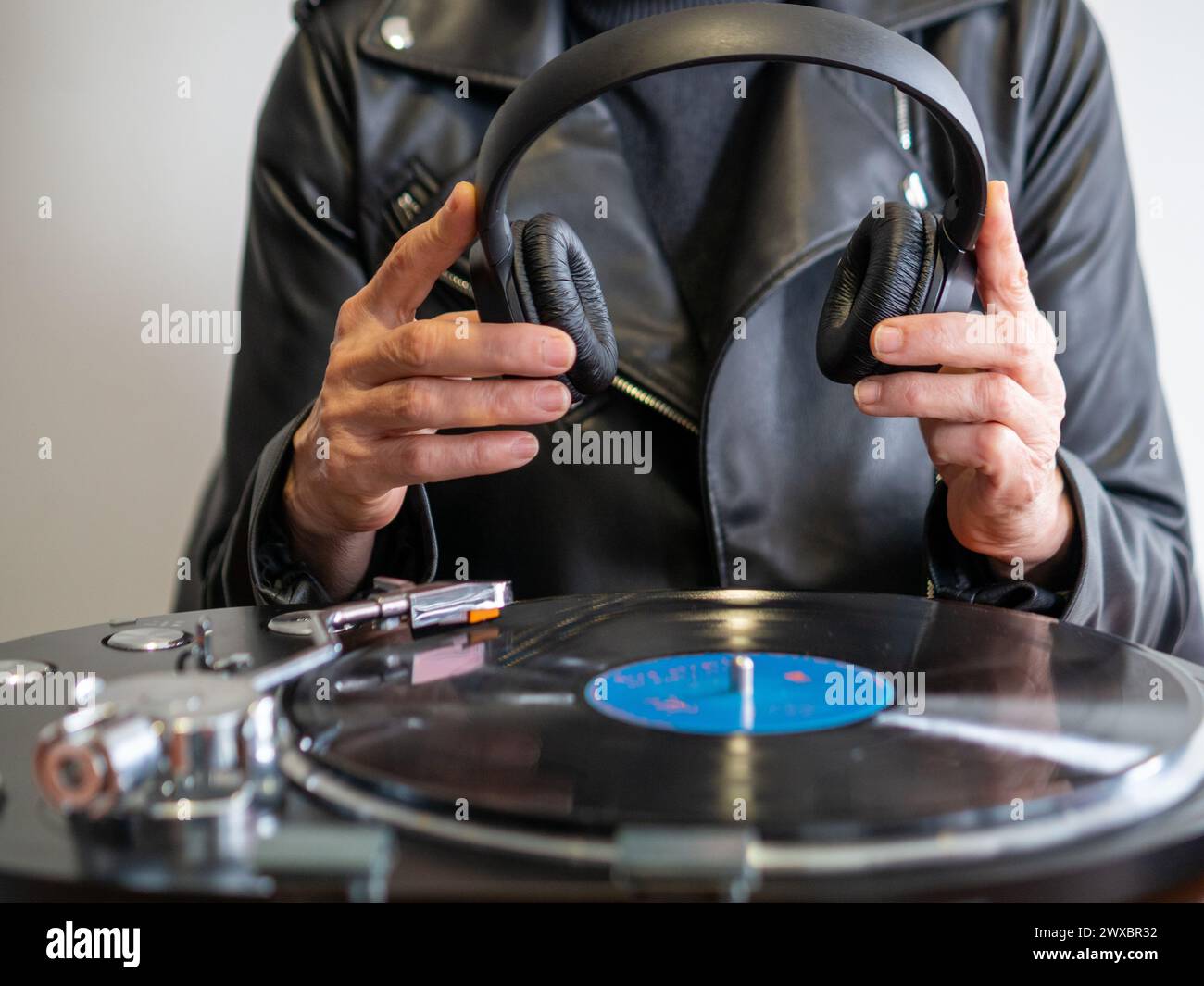A lady wearing a leather jacket holding to use her headphones while her ...