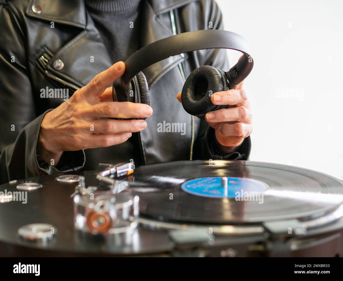 A lady wearing a leather jacket holding to use her headphones while her ...