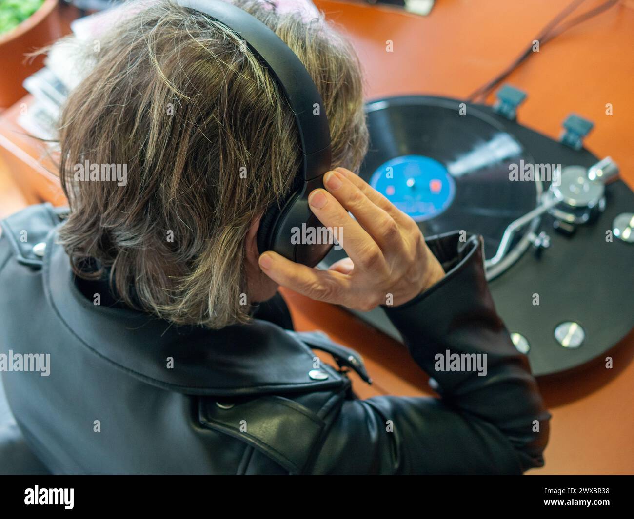 An unrecognizible lady putting on her headphone while her turntable is ...