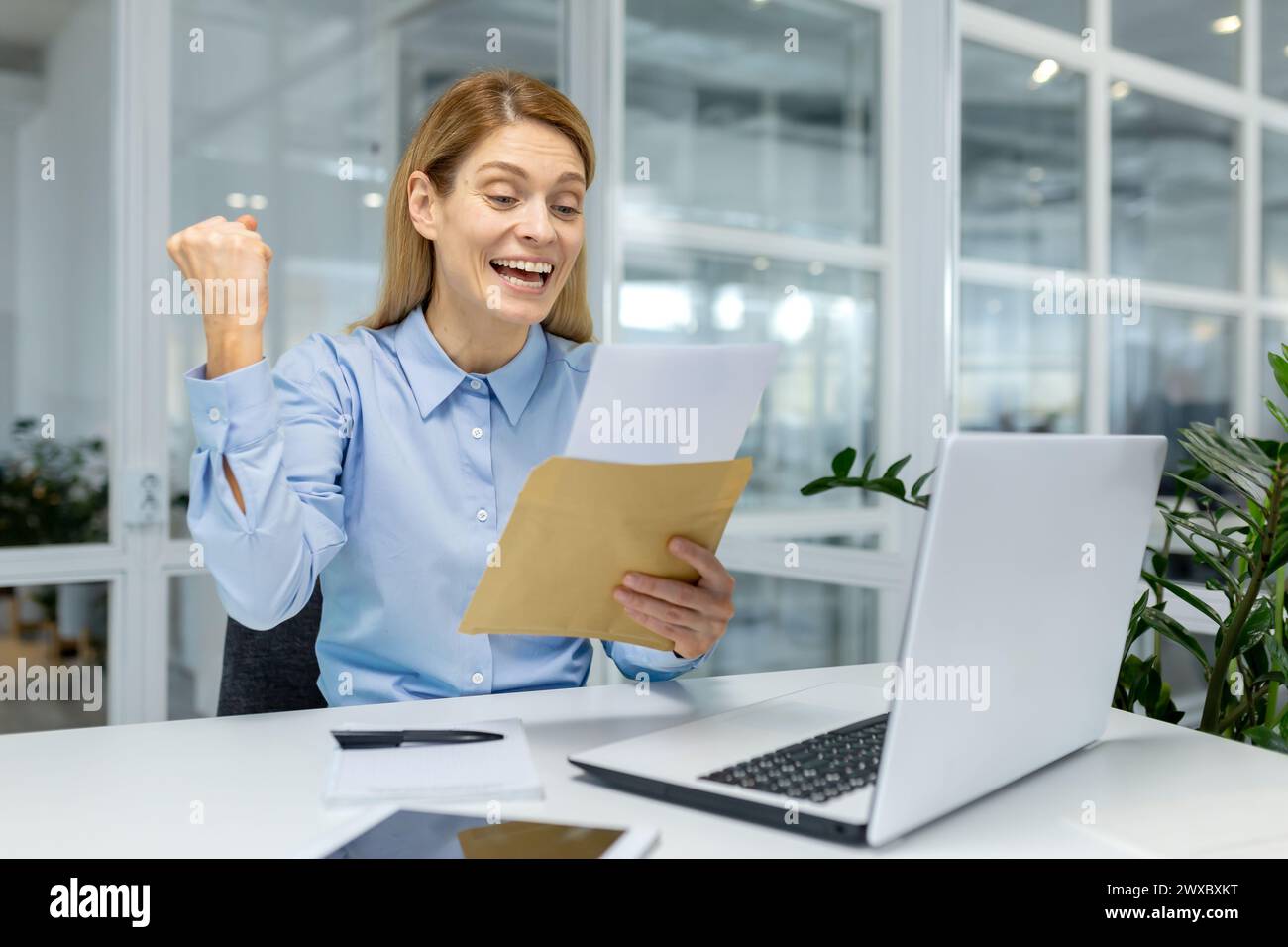 A joyful female office worker celebrates success with an envelope in a ...
