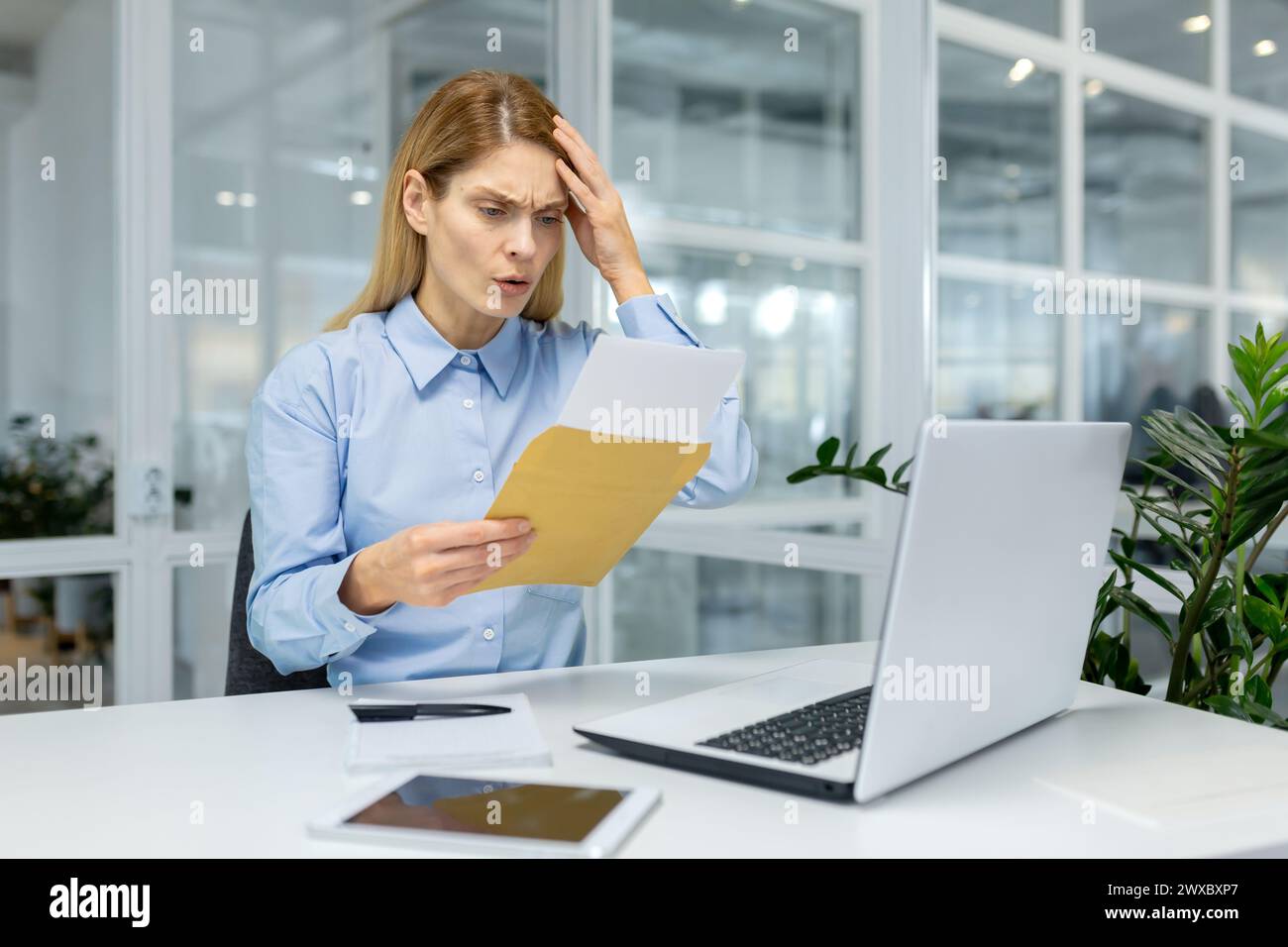 A businesswoman in a blue shirt appears perplexed analyzing documents ...