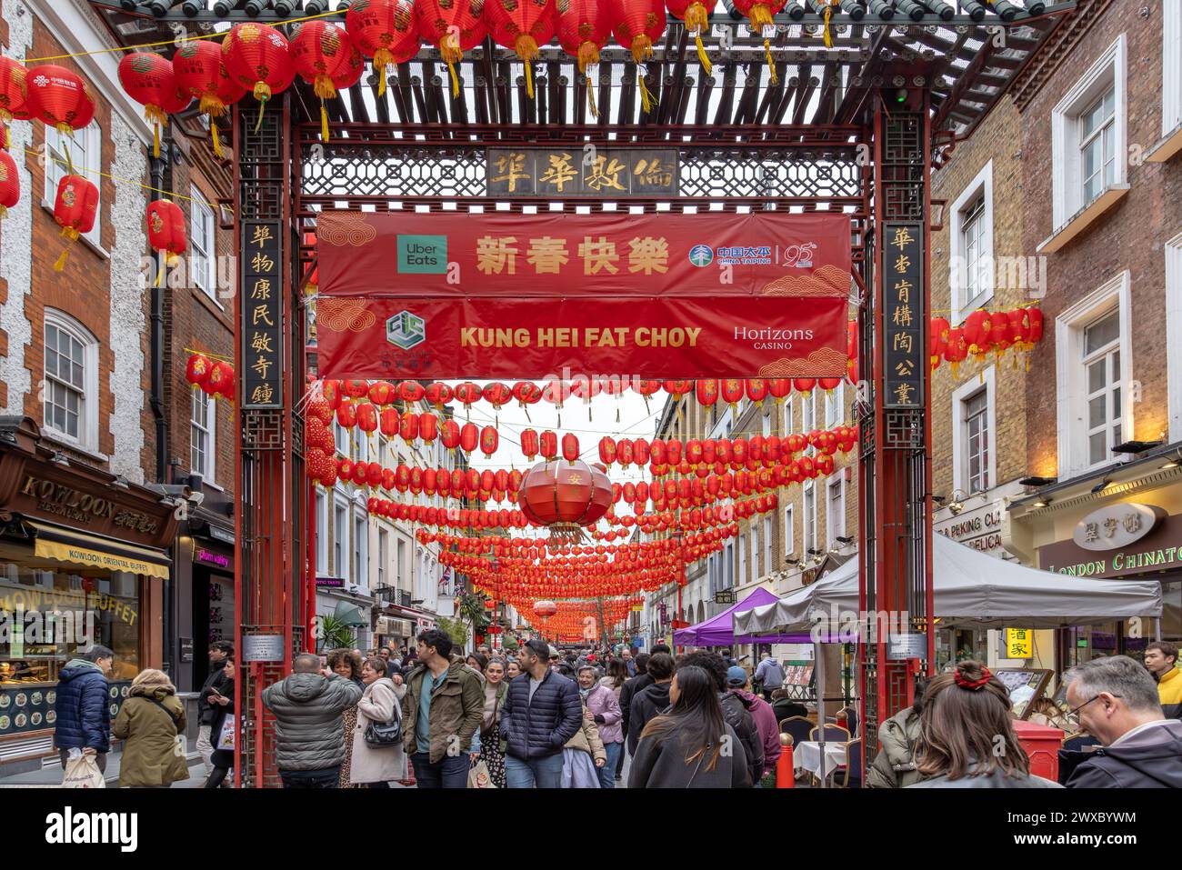 The bustle of shoppers and tourists beneath the colourful Chinese gate, red lanterns and banners ...