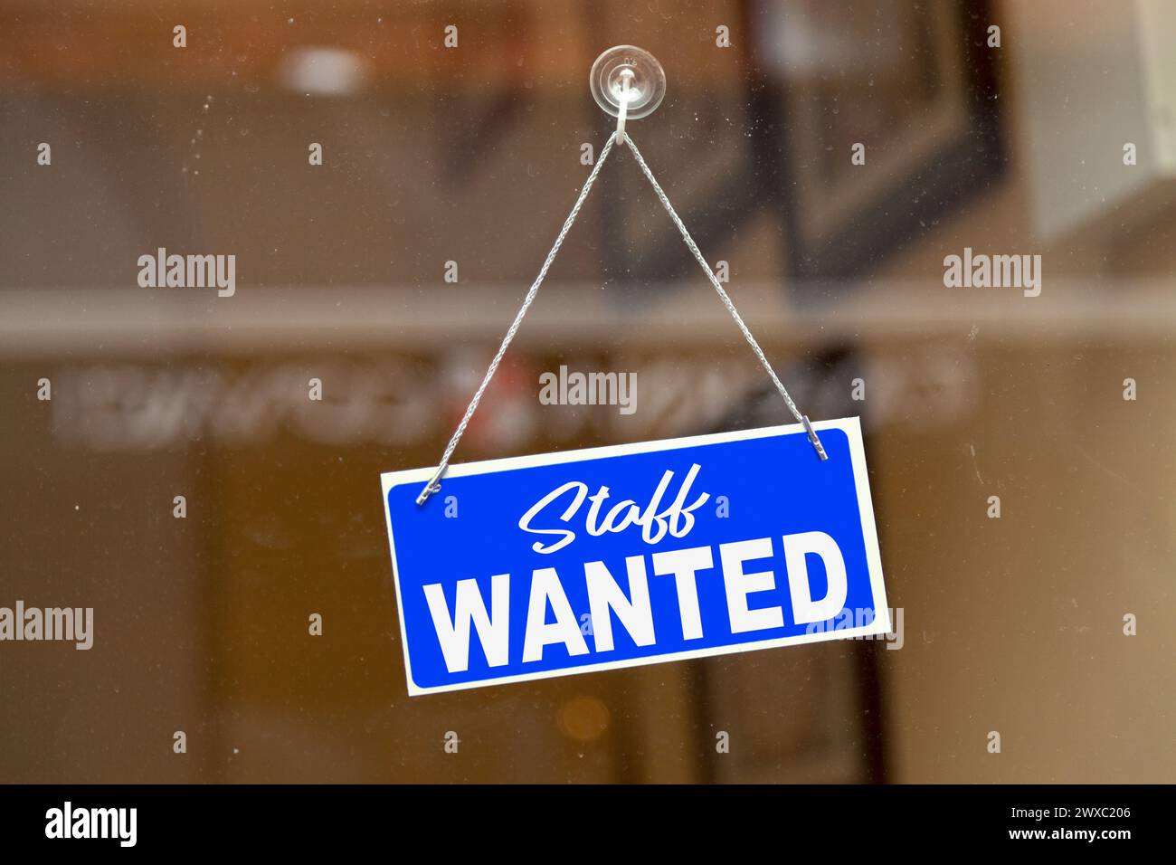 Blue sign hanging at the glass door of a shop saying: "Staff wanted ...
