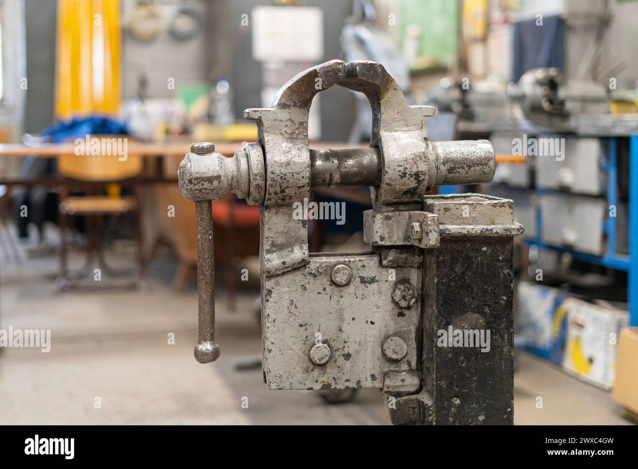 An old, worn, gray-painted large vise on a stand in the middle of an ...