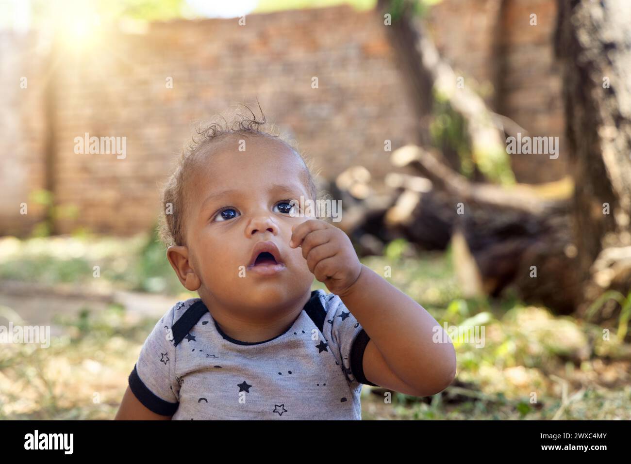 african baby standing in the yard at sunset, brick wall in the ...