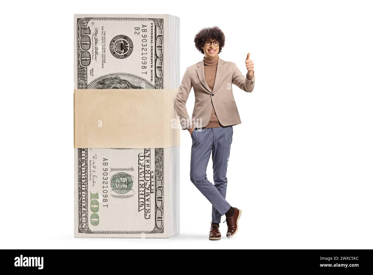 Young man leaning on a stack of money and gesturing thumbs up isolated ...