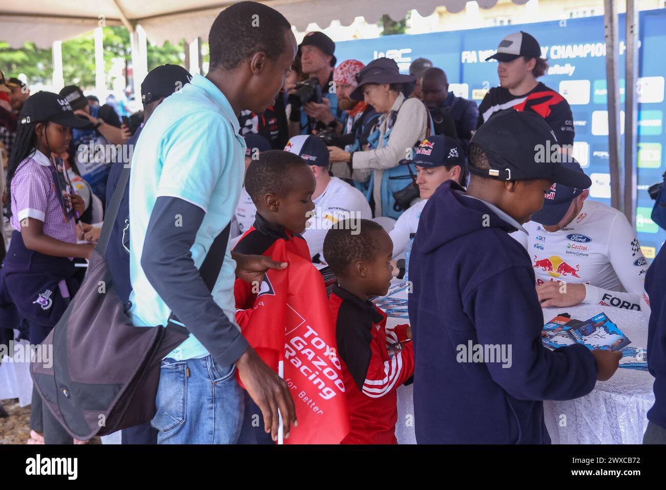 A Kenyan man with his children line up to get autographs from rally ...