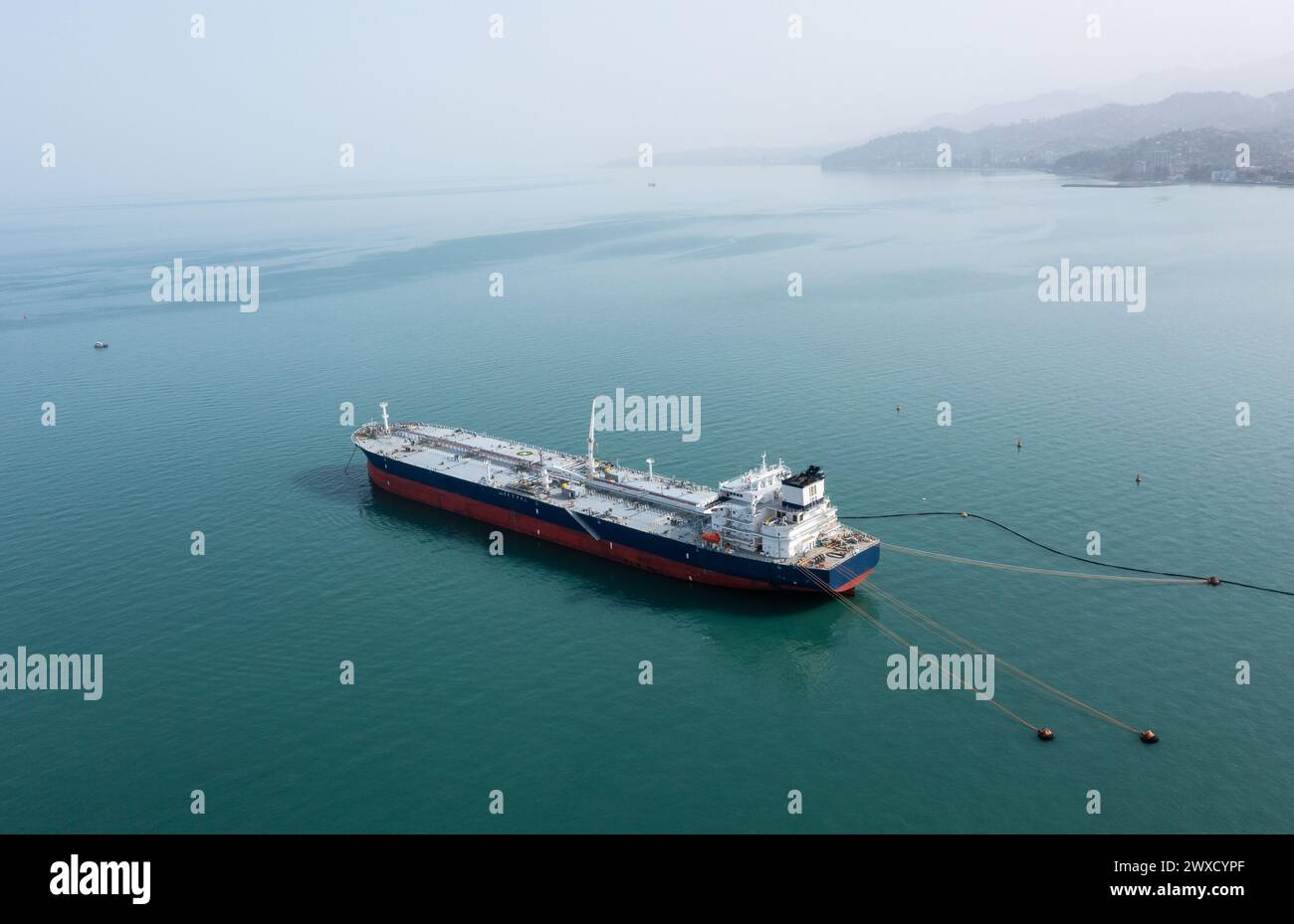 Aerial shot of a massive oil tanker anchored offshore near a coastal ...