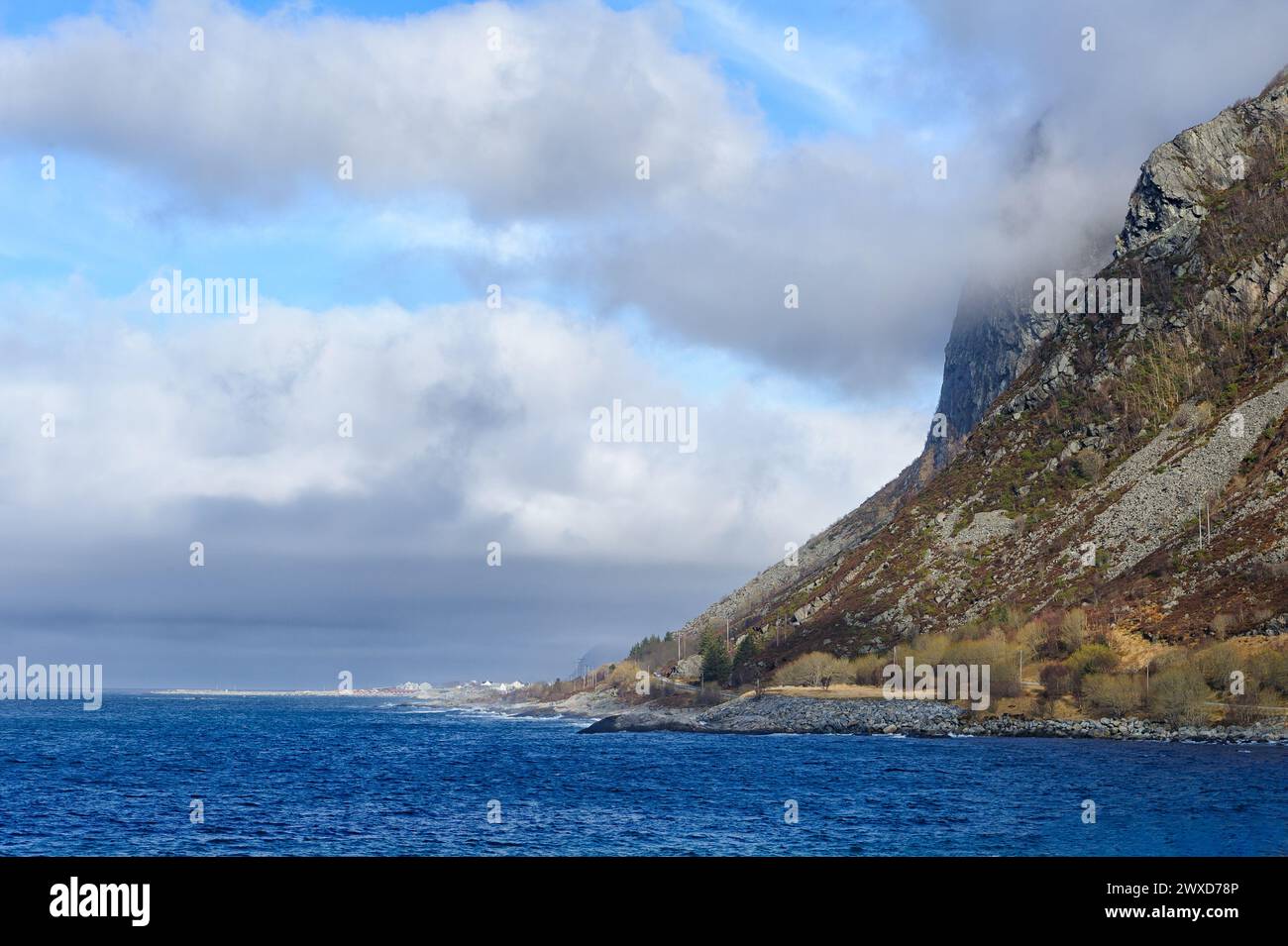 A looming mountain cliff extends into the ocean, partly shrouded by ...