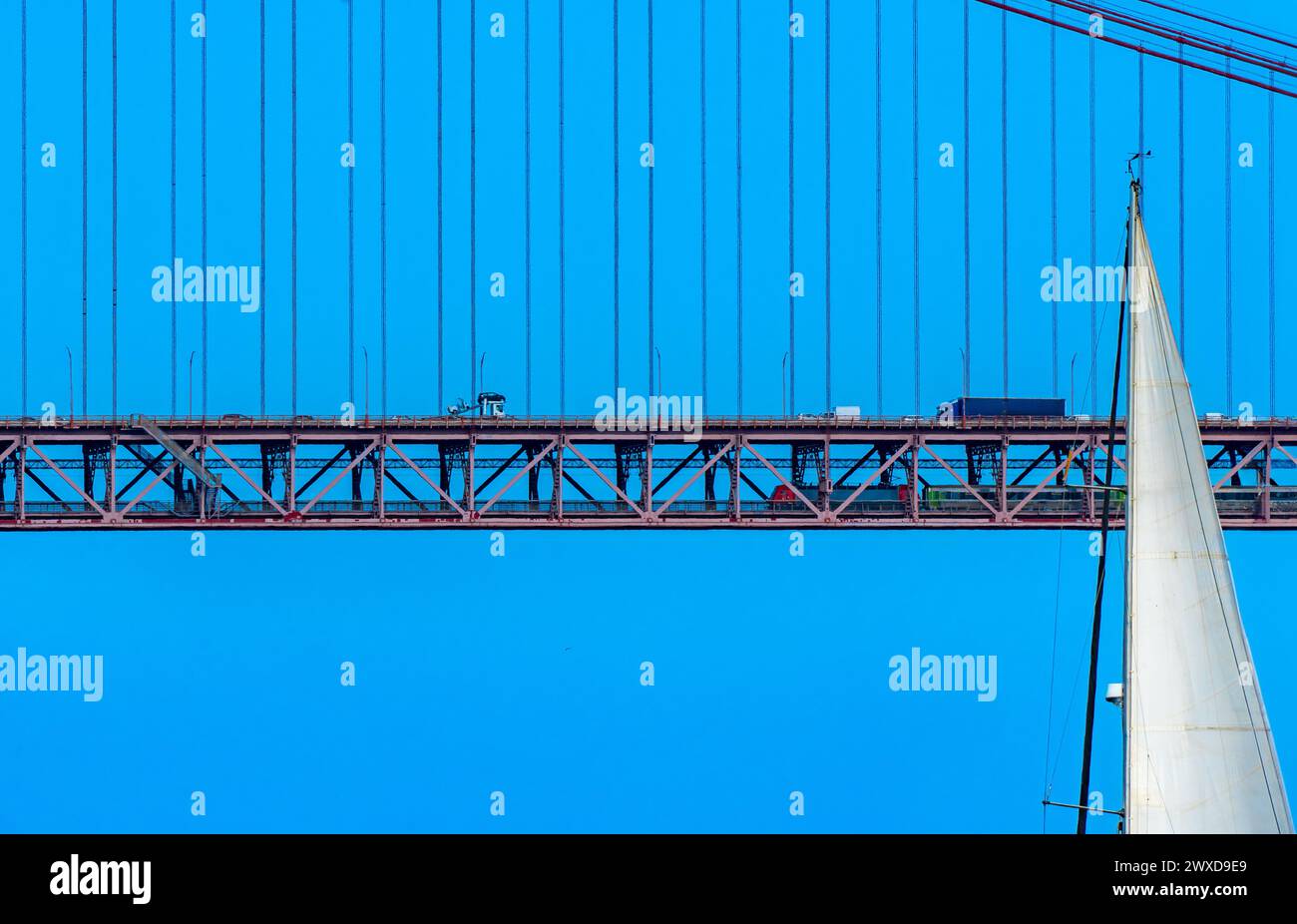 Top of the white sail of a sailboat sailing in front of the red steel ...