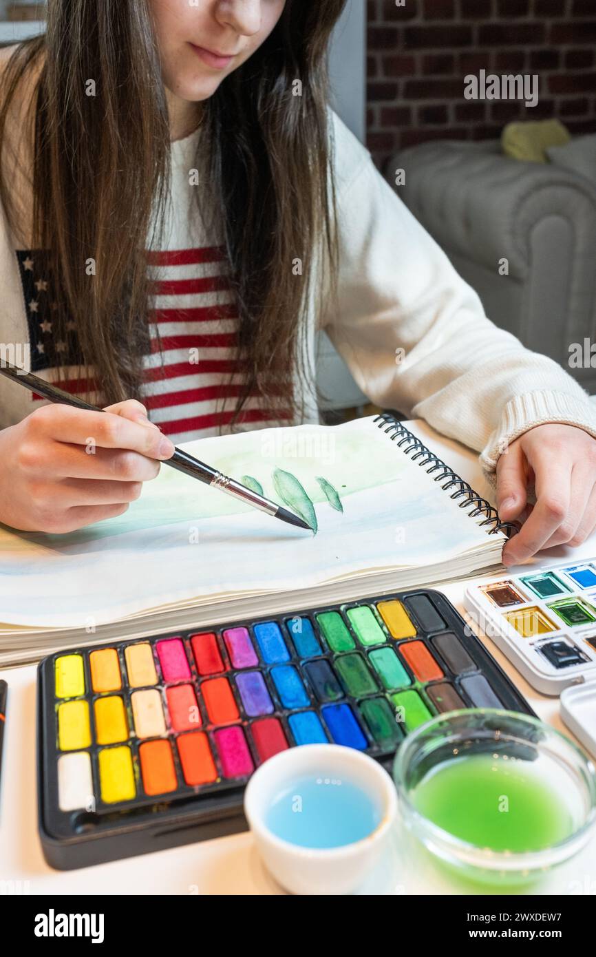 Front view of a woman's hand painting a landscape with watercolors on a ...