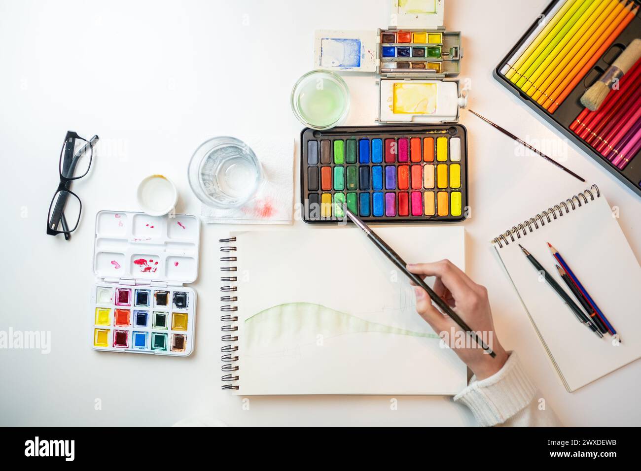 Top view of a woman's hand picking up watercolor paint with a brush. In ...