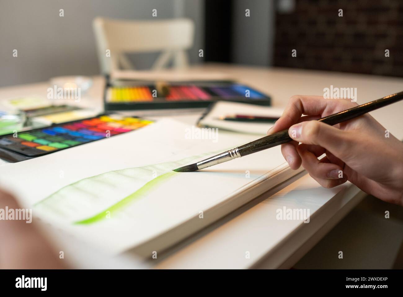 Side view of a woman's hand picking up watercolor paint with a brush ...