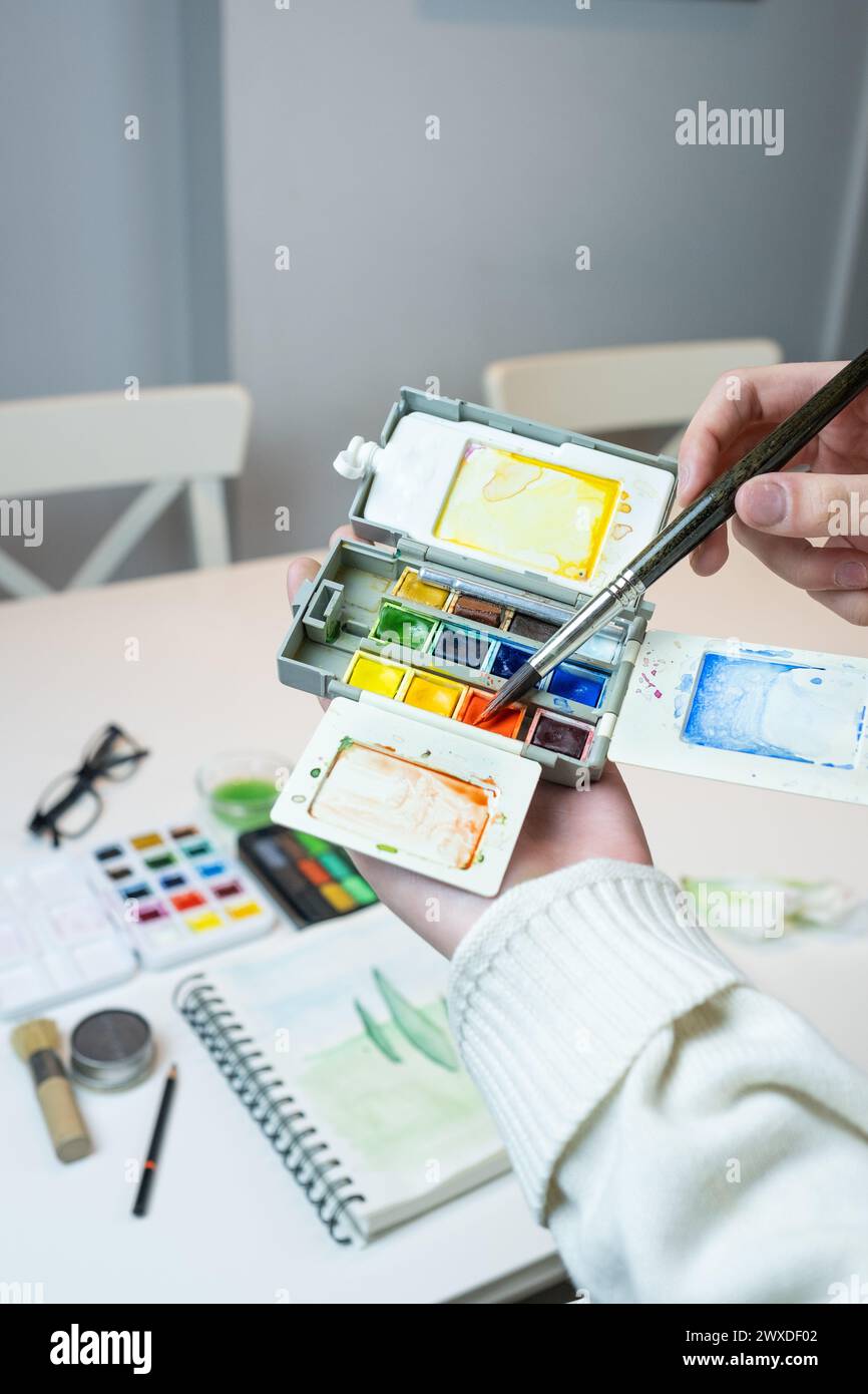 Detail of a watercolor field kit. a hand of a woman is picking up some ...