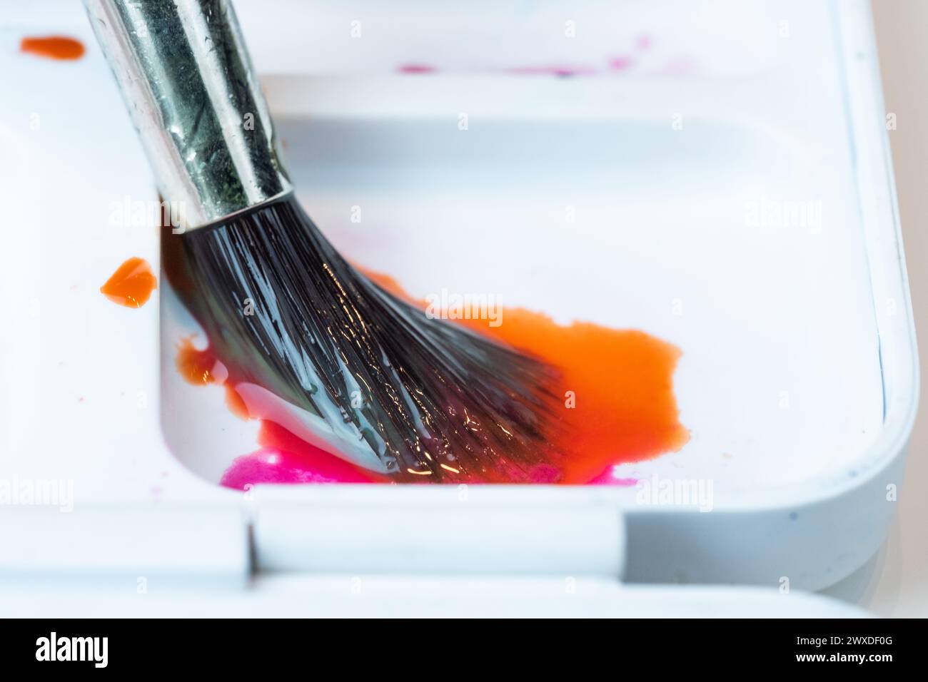 Detail of A brush mixing orange and red watercolors to get a gbright ...