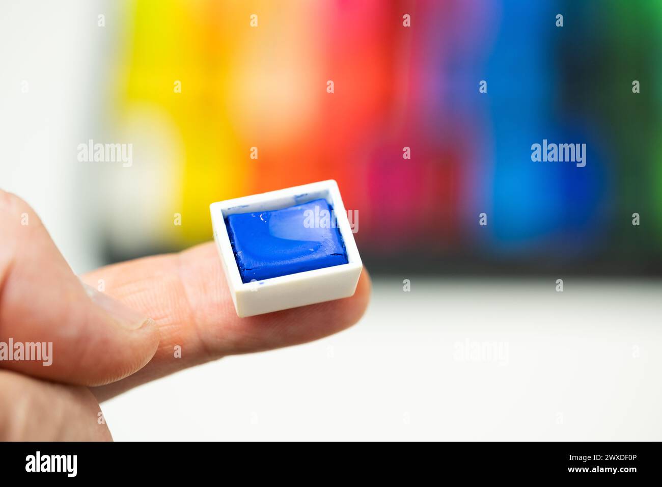 A finger showing a mini blue watercolor cube with a multicolored ...