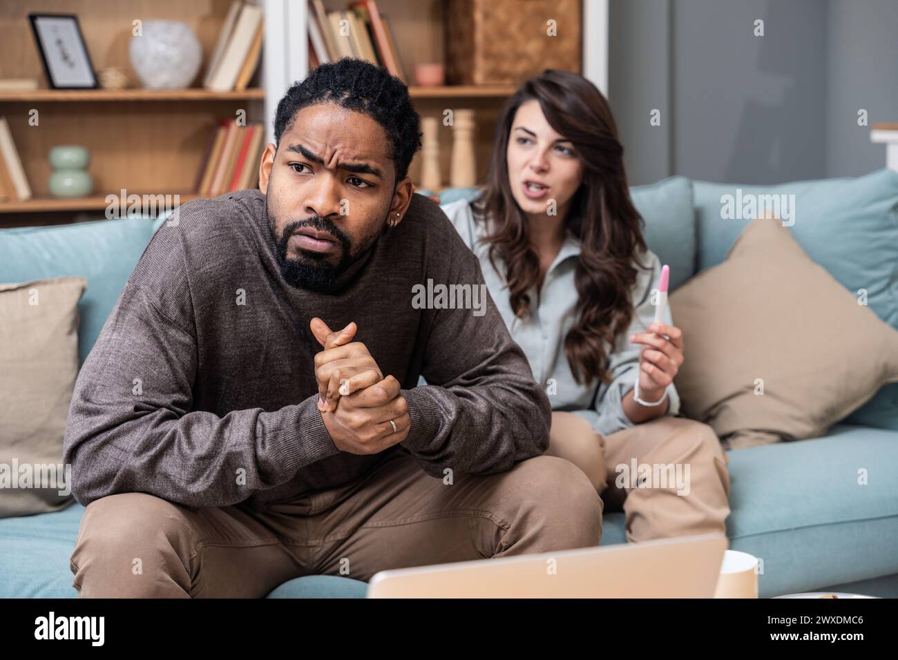Unhappy Young Woman Sitting On Sofa With Pregnancy Test And African