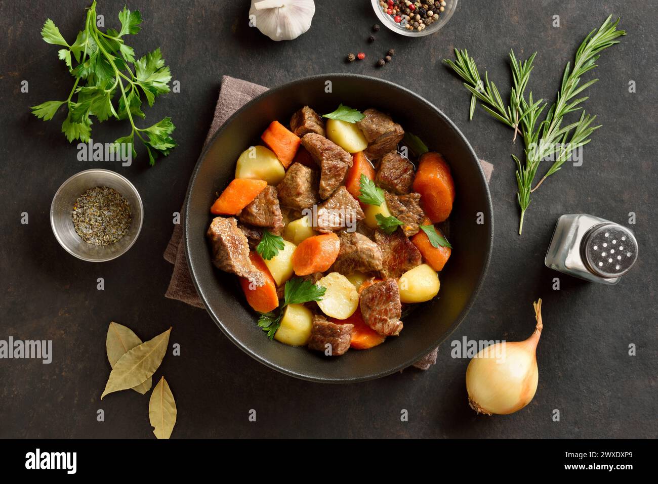 Beef stew with potatoes, carrots and greens in bowl over dark stone ...