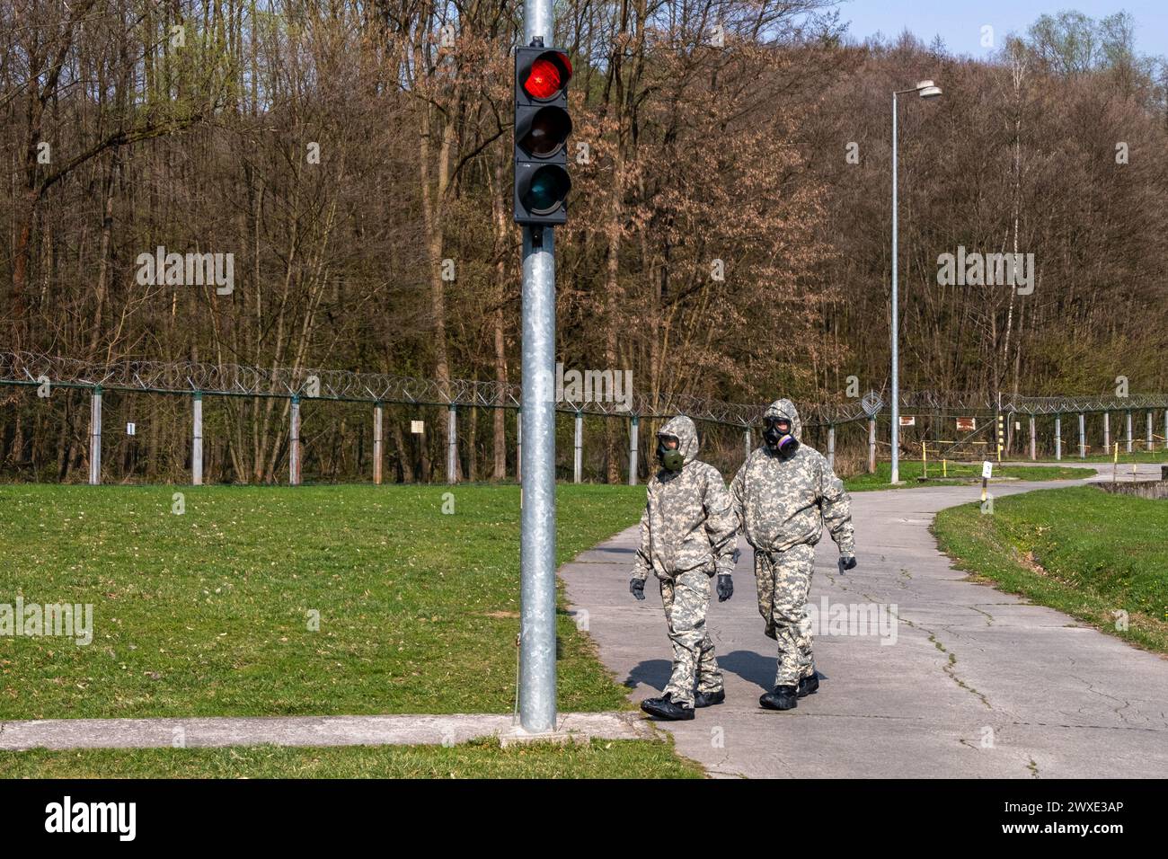Two men in camouflage walk across a path next to a traffic light. The ...