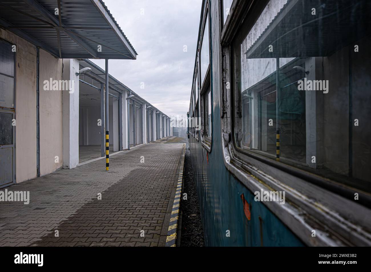 A train is parked at a station with a brick walkway. The train is blue ...