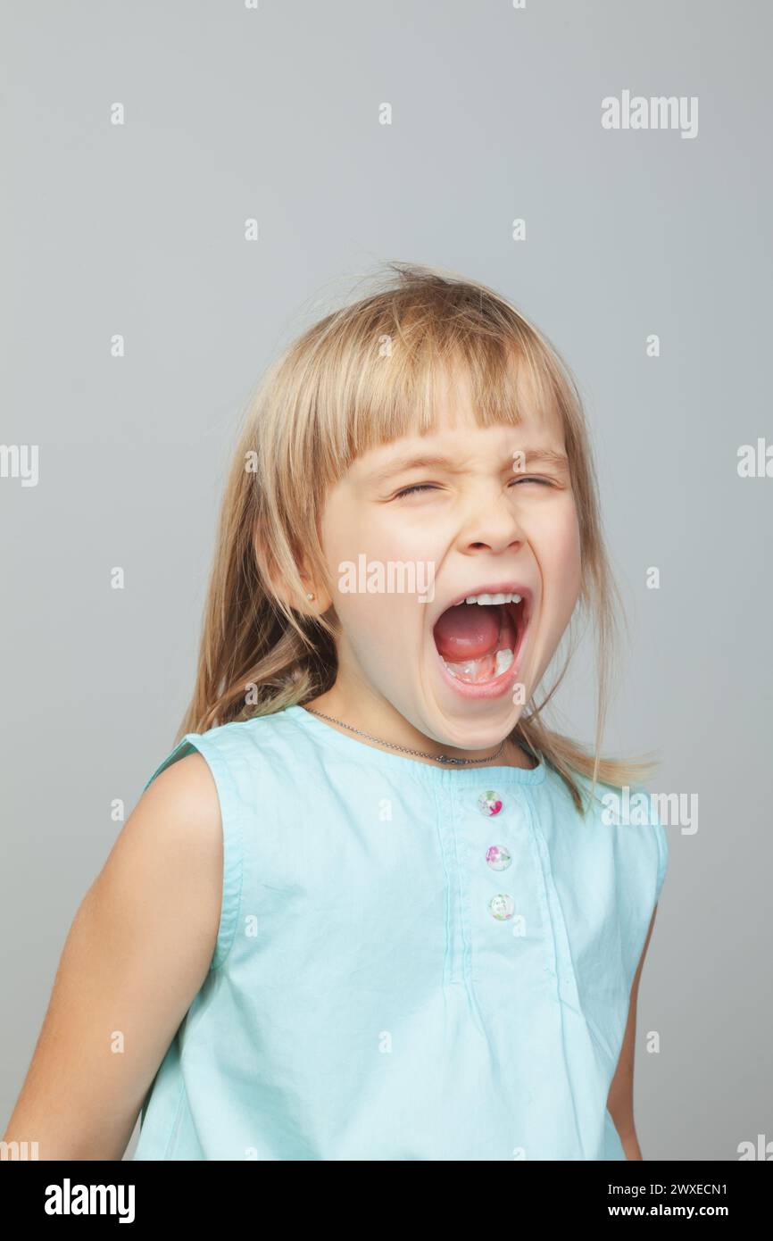 A young girl wearing blue dress screaming with eyes closed. Studio ...