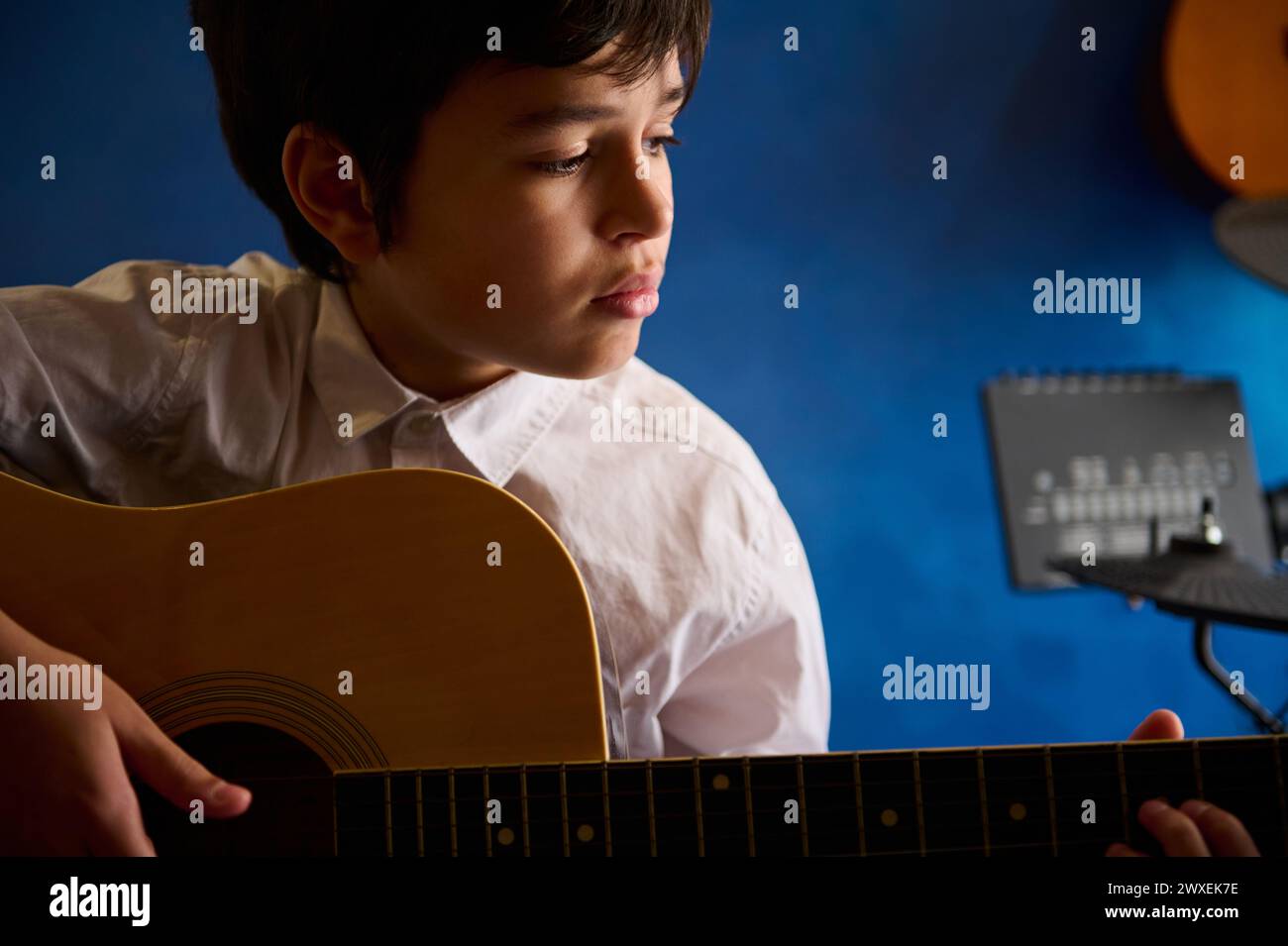 Hispanic teenage boy playing acoustic guitar at home, sitting against ...