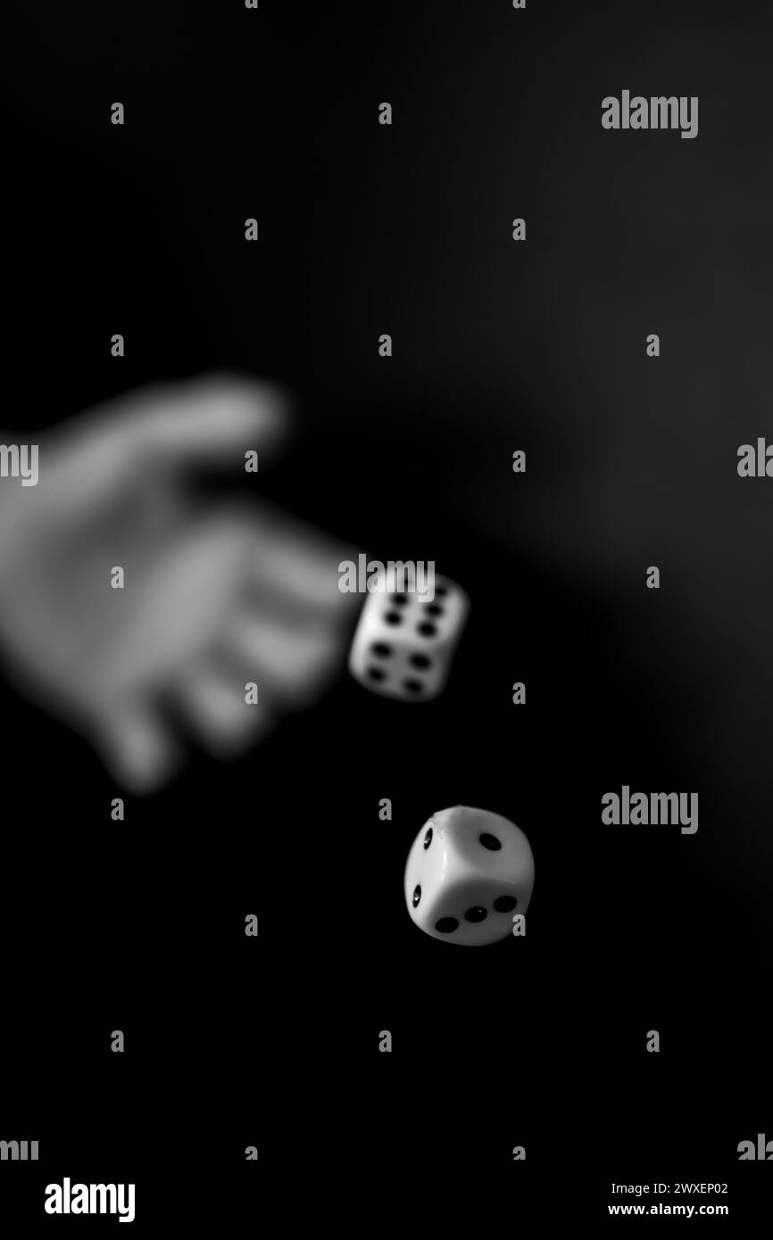 Hand rolling two dice against a black background Stock Photo - Alamy