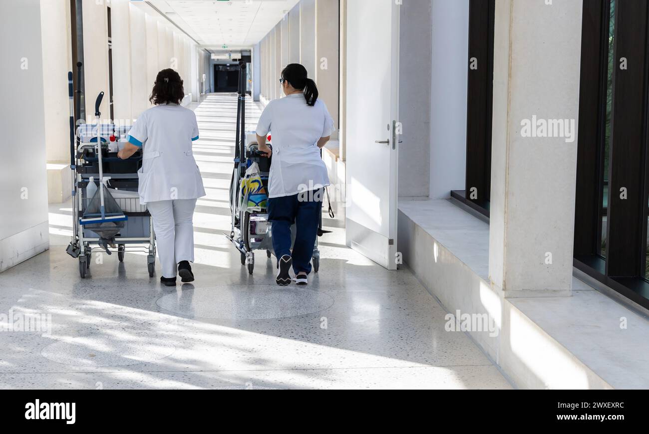 Two female cleaners with cleaning carts walk along a long white ...