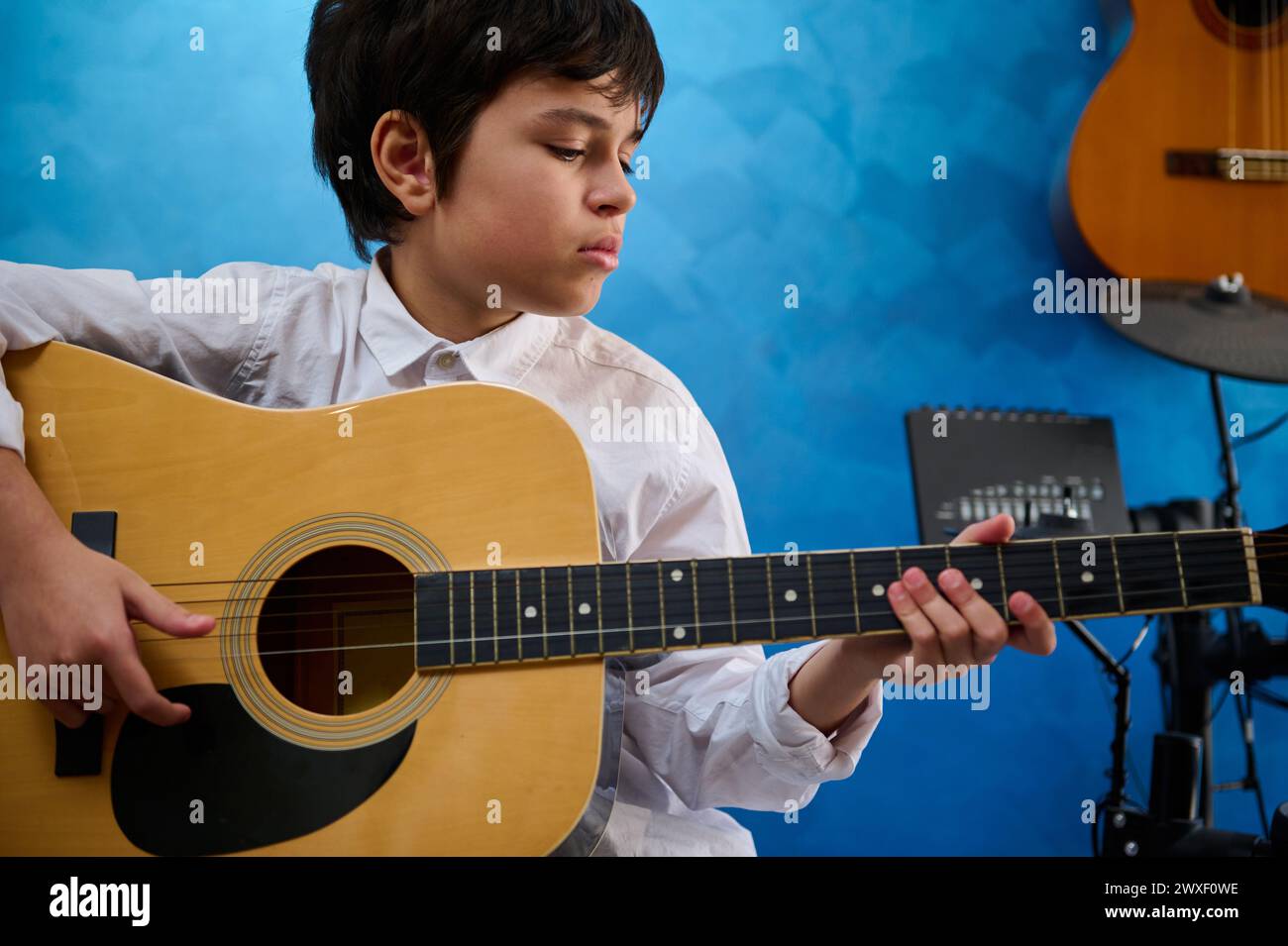 Adorable Caucasian teenager boy playing acoustic guitar in a music ...
