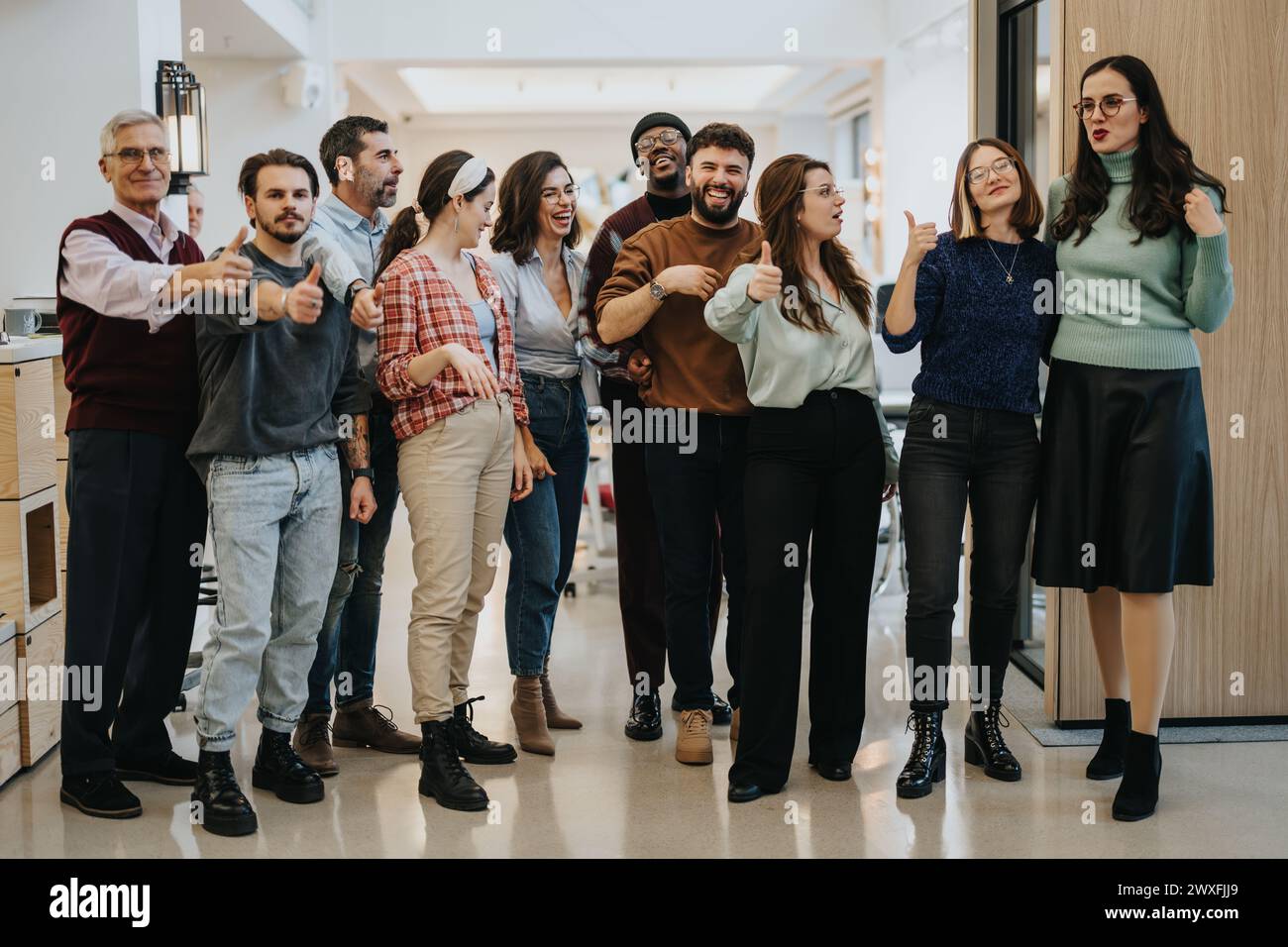 Cross generational group of people giving thumbs up in a modern office ...