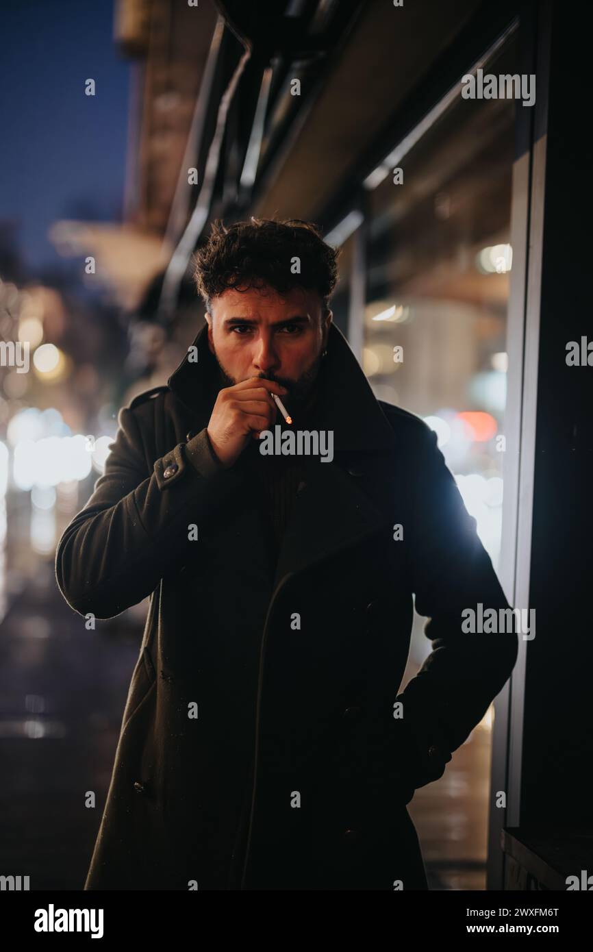 Good looking man smoking a cigarette on a rainy night in the urban city ...