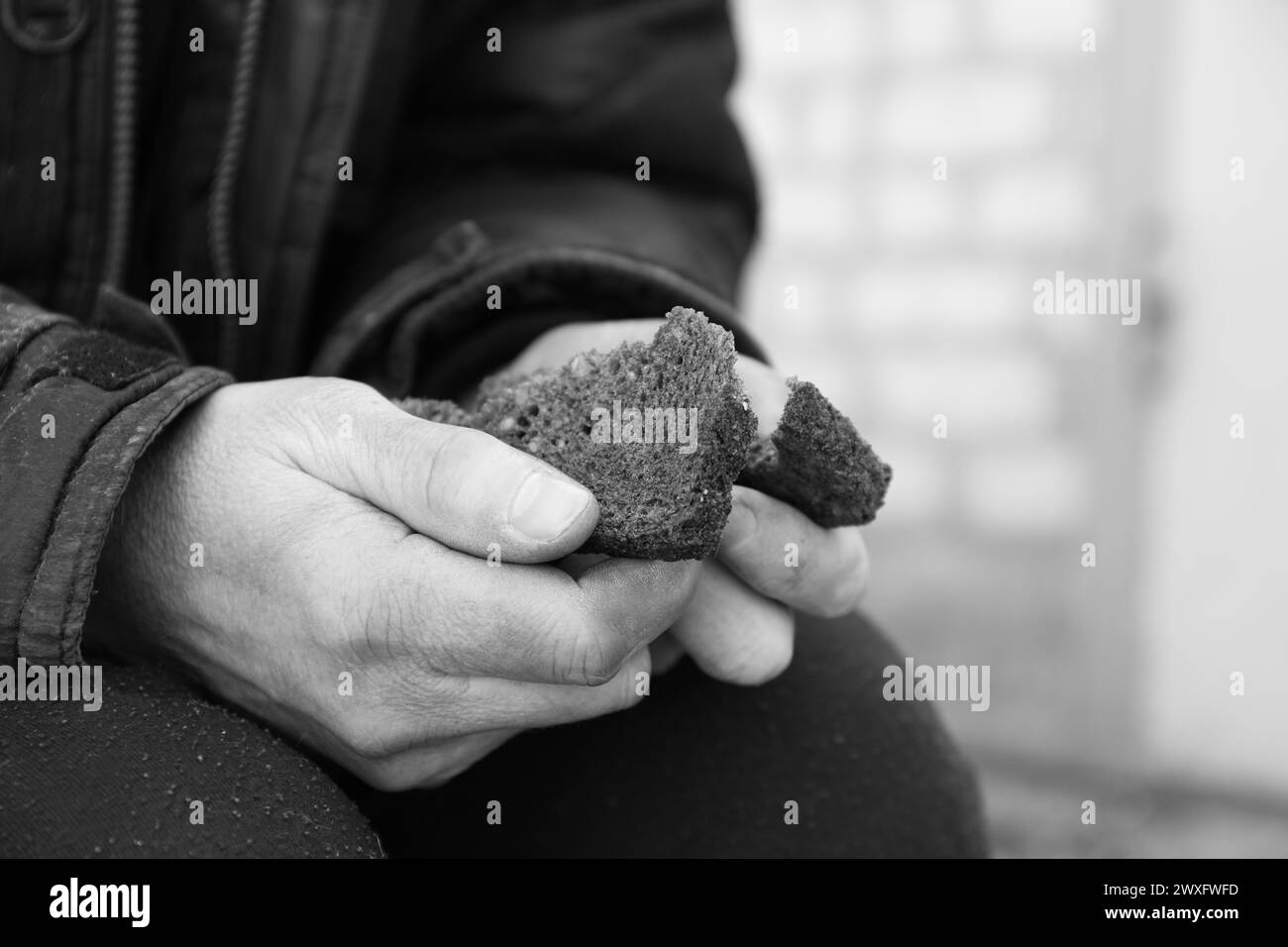 Poor homeless man holding piece of bread outdoors, closeup. Black and ...