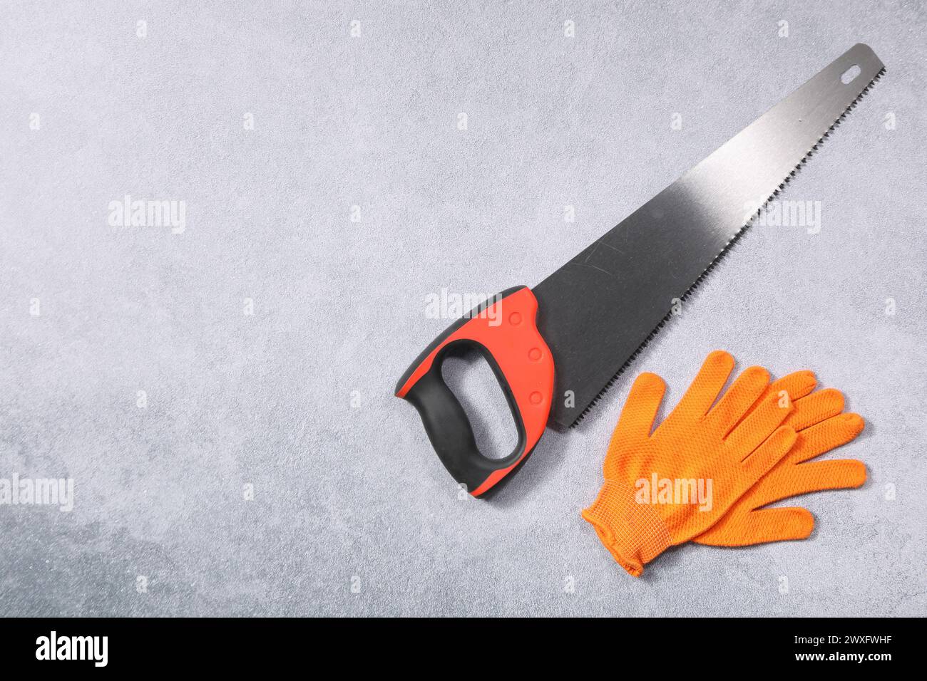 Saw with colorful handle and gloves on gray background, flat lay. Space ...