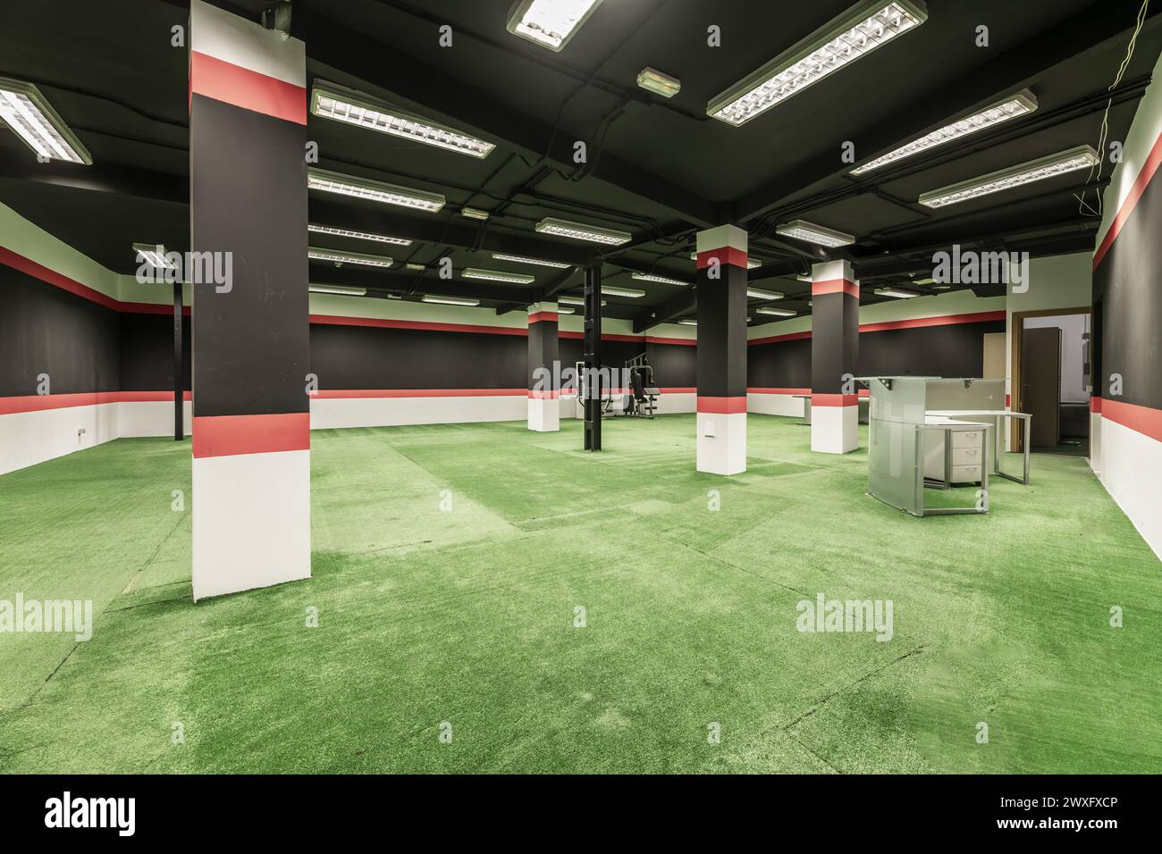 Large, half-empty gym with artificial grass floor, a counter, and black ...