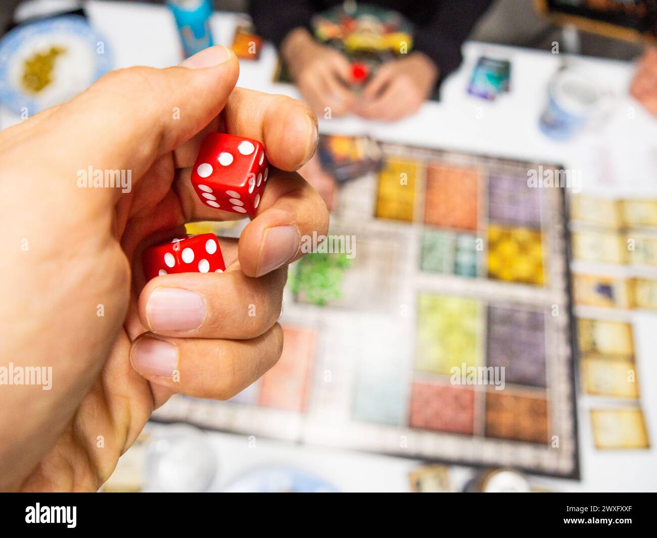Hand with red six-sided dice on game board from above with other real ...