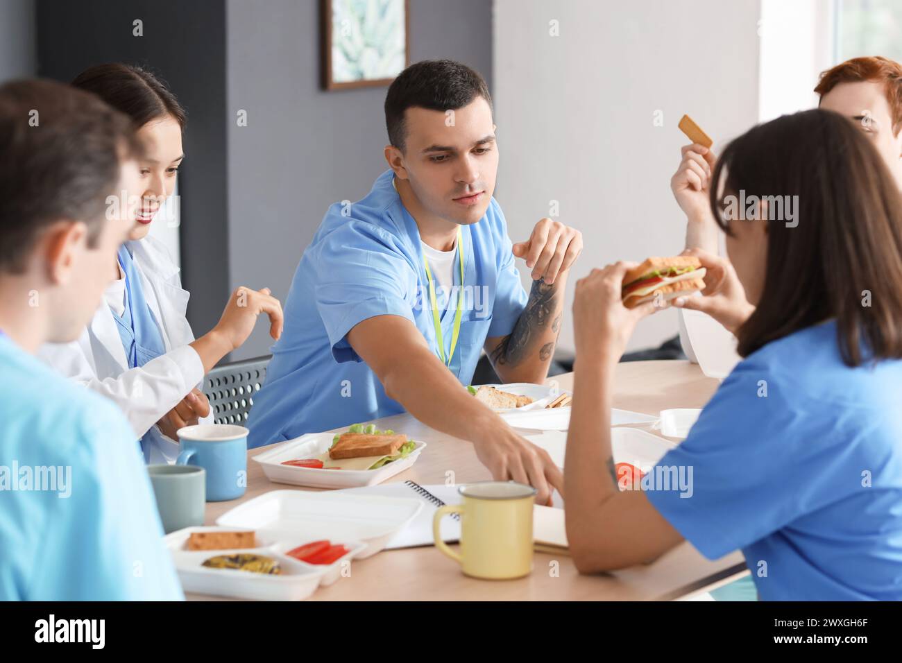 Male doctor having lunch at table with his colleagues in hospital ...