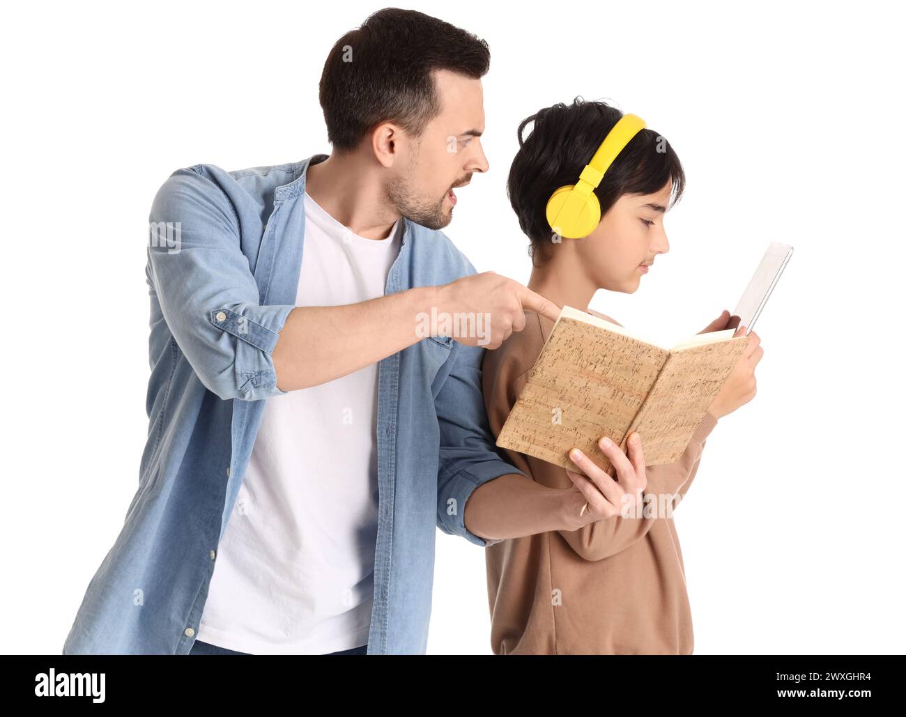 Angry father pointing at book and his teenage son using tablet computer ...
