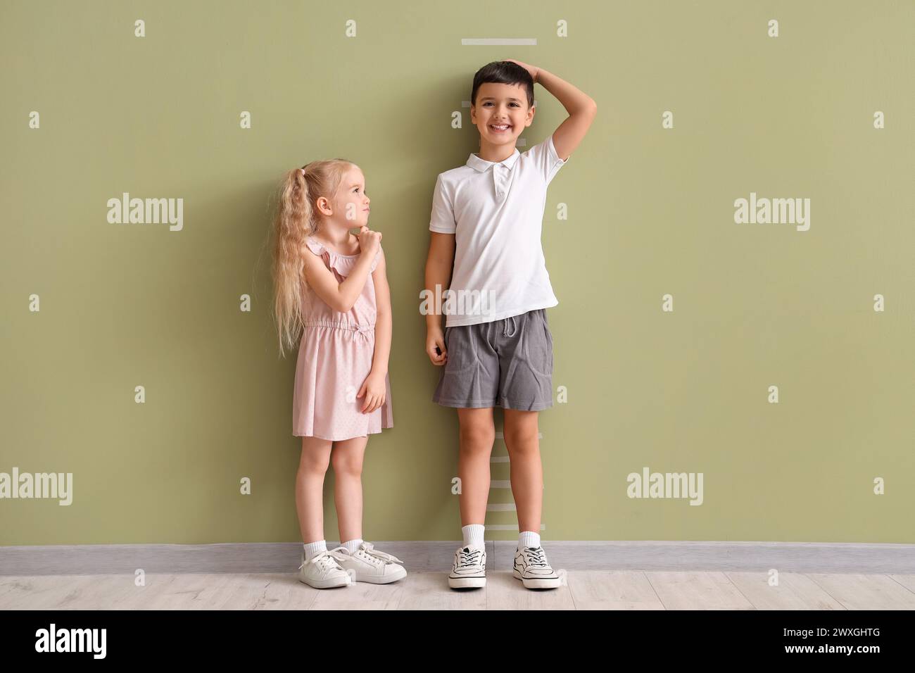 Cute little kids measuring height near green wall Stock Photo - Alamy