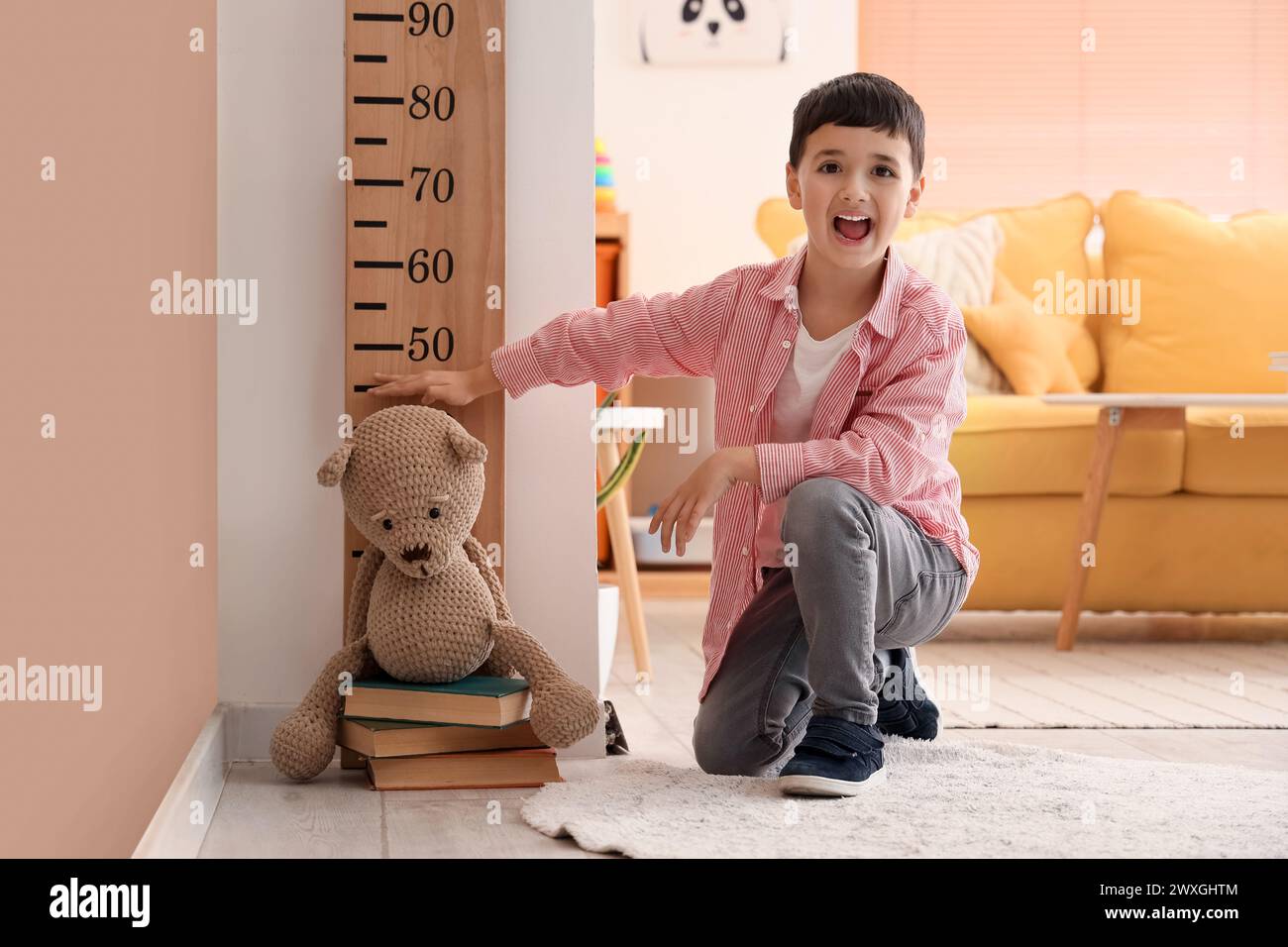 Cute little boy measuring height of plush toy near wooden stadiometer ...