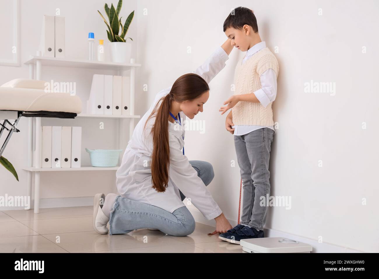 Pediatrician measuring height of cute little boy near white wall in ...
