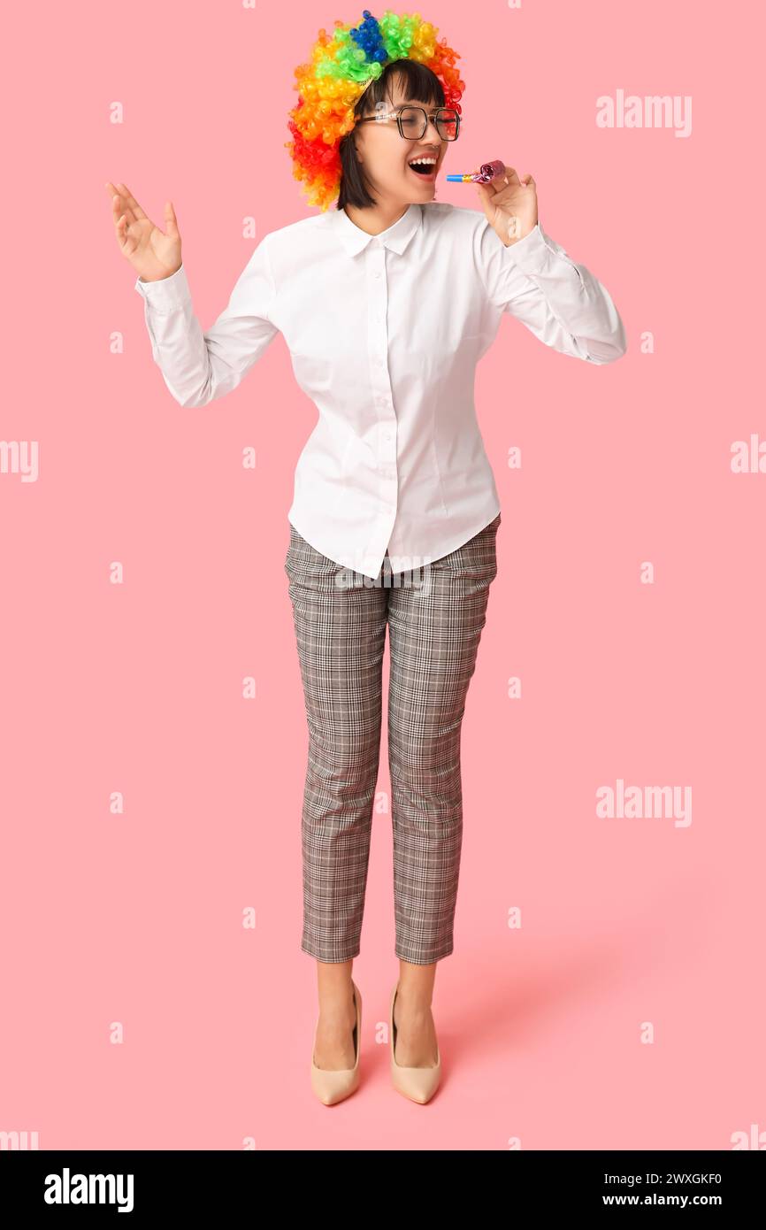 Funny young businesswoman with party blower on pink background. Fool's ...