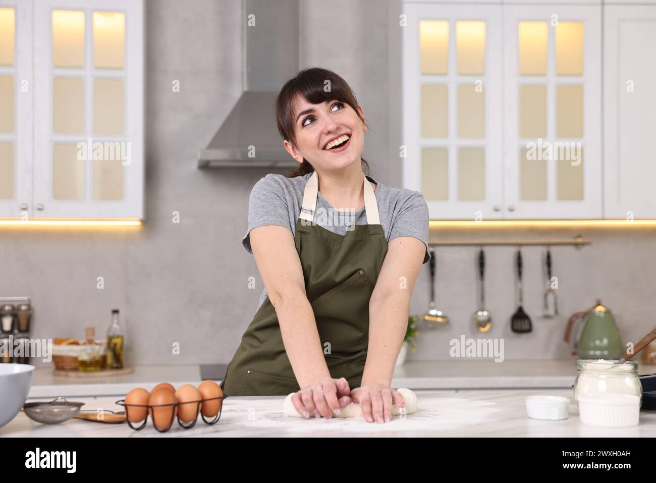 Happy young housewife kneading dough at white table in kitchen Stock ...
