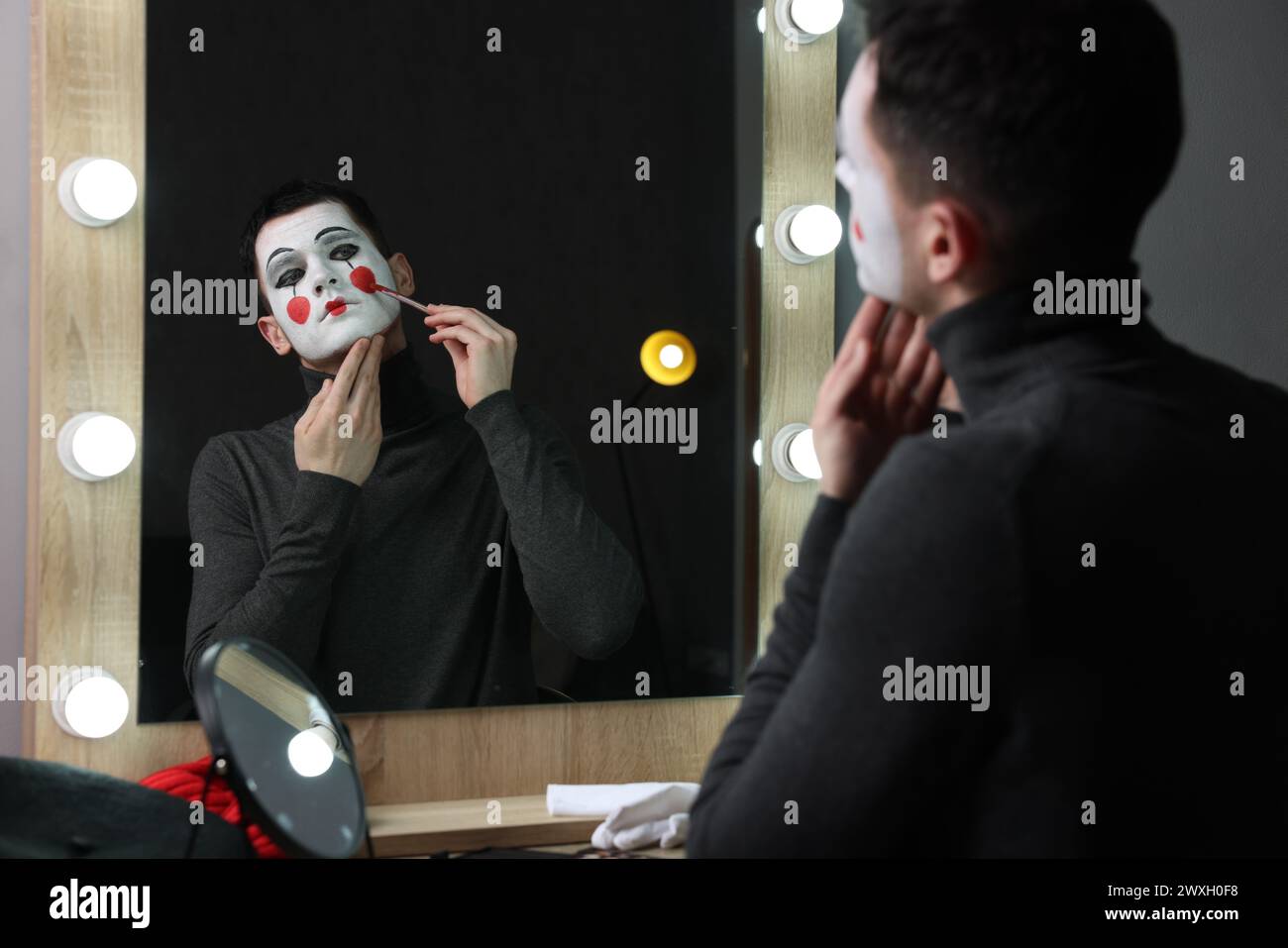 Young man applying mime makeup near mirror in dressing room Stock Photo - Alamy