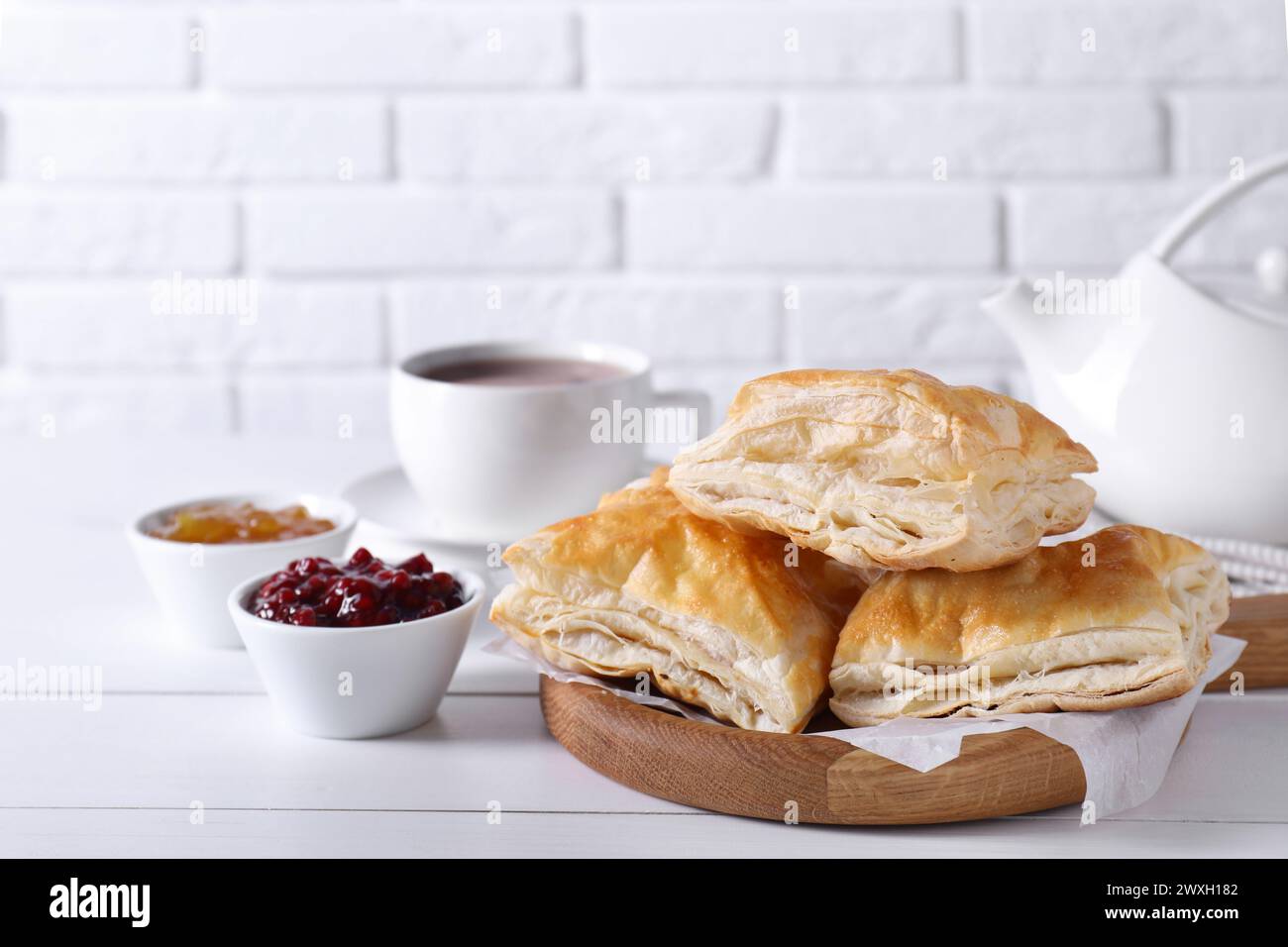Delicious puff pastry served on white wooden table against brick wall ...