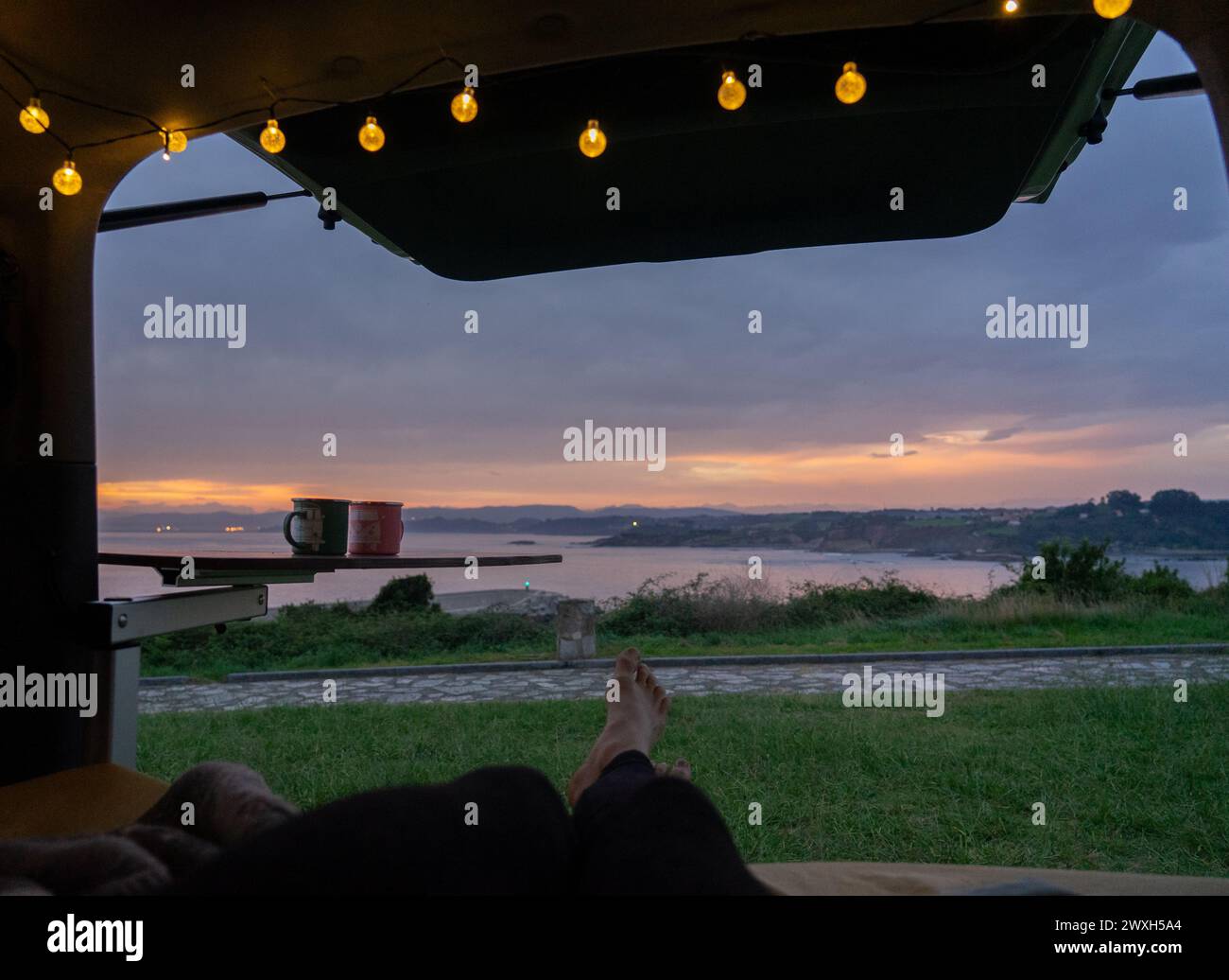 Woman's feet inside a camper van with sunrise views and a few cups of ...