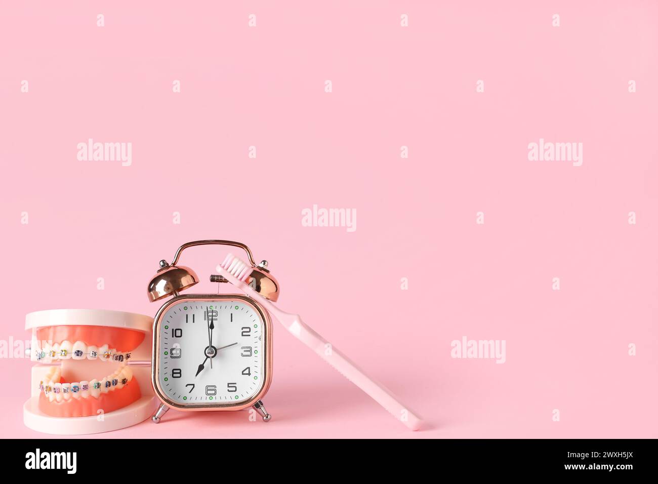 Alarm clock, model of jaw with dental braces and toothbrush on pink ...
