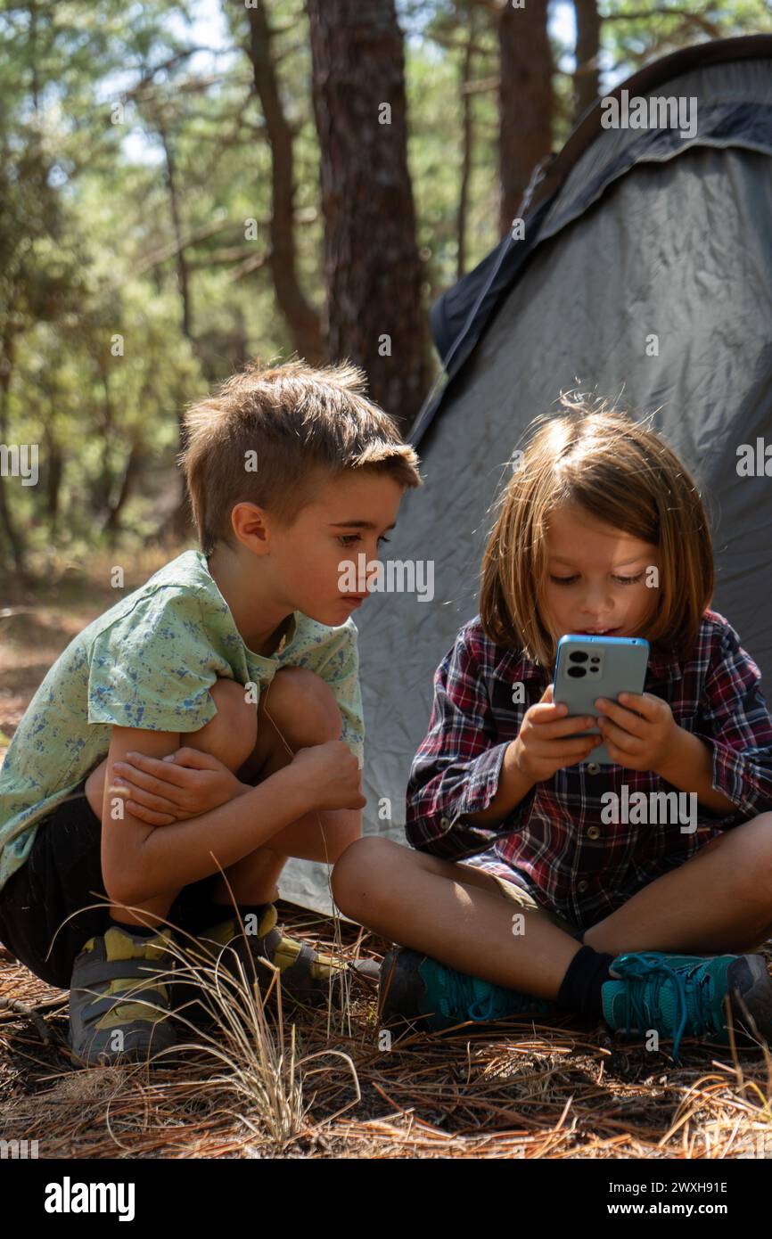Two children camping in the woods looking at their smartphone Stock ...