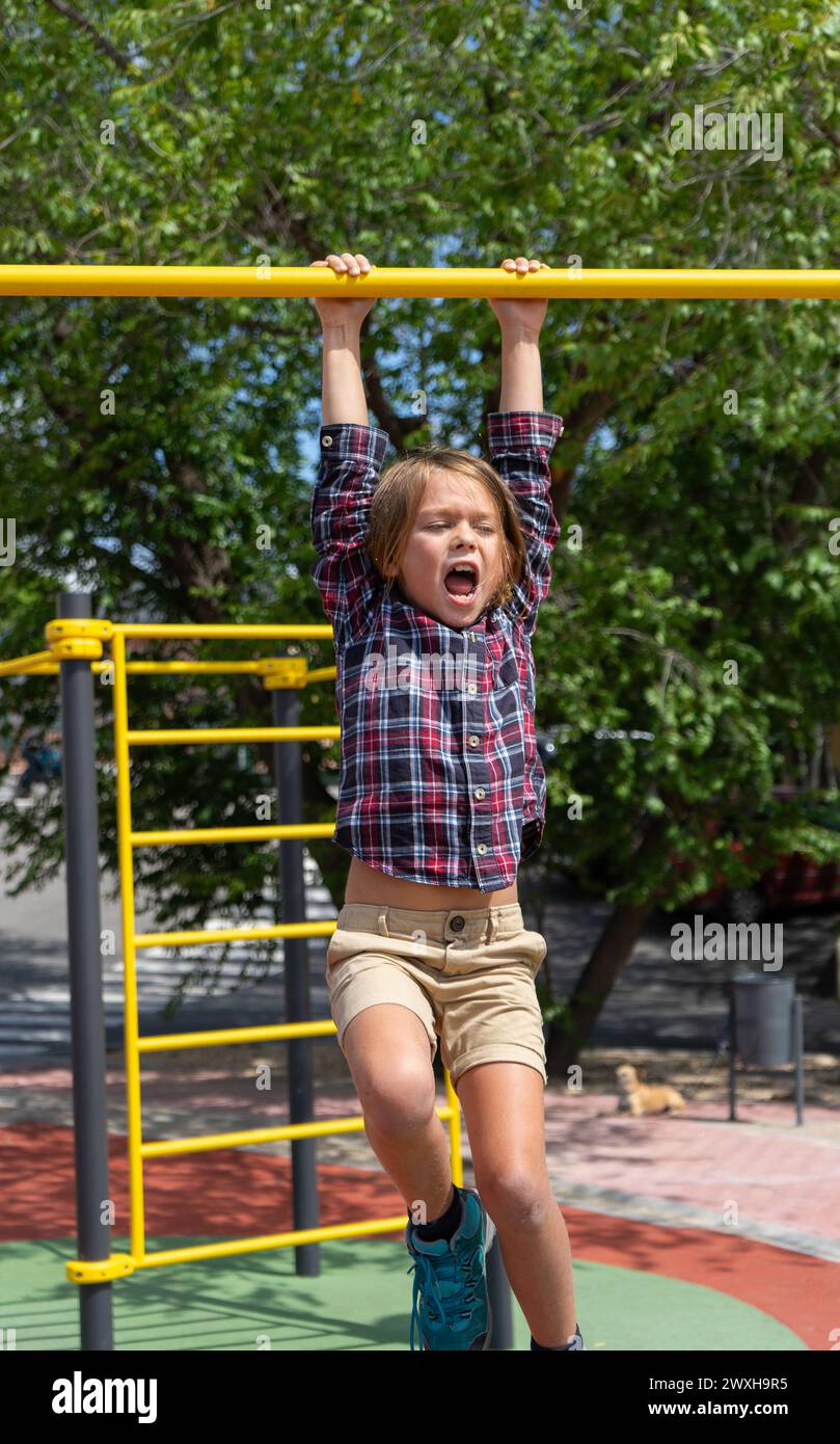 Boy hanging from an exercise bar screaming Stock Photo - Alamy